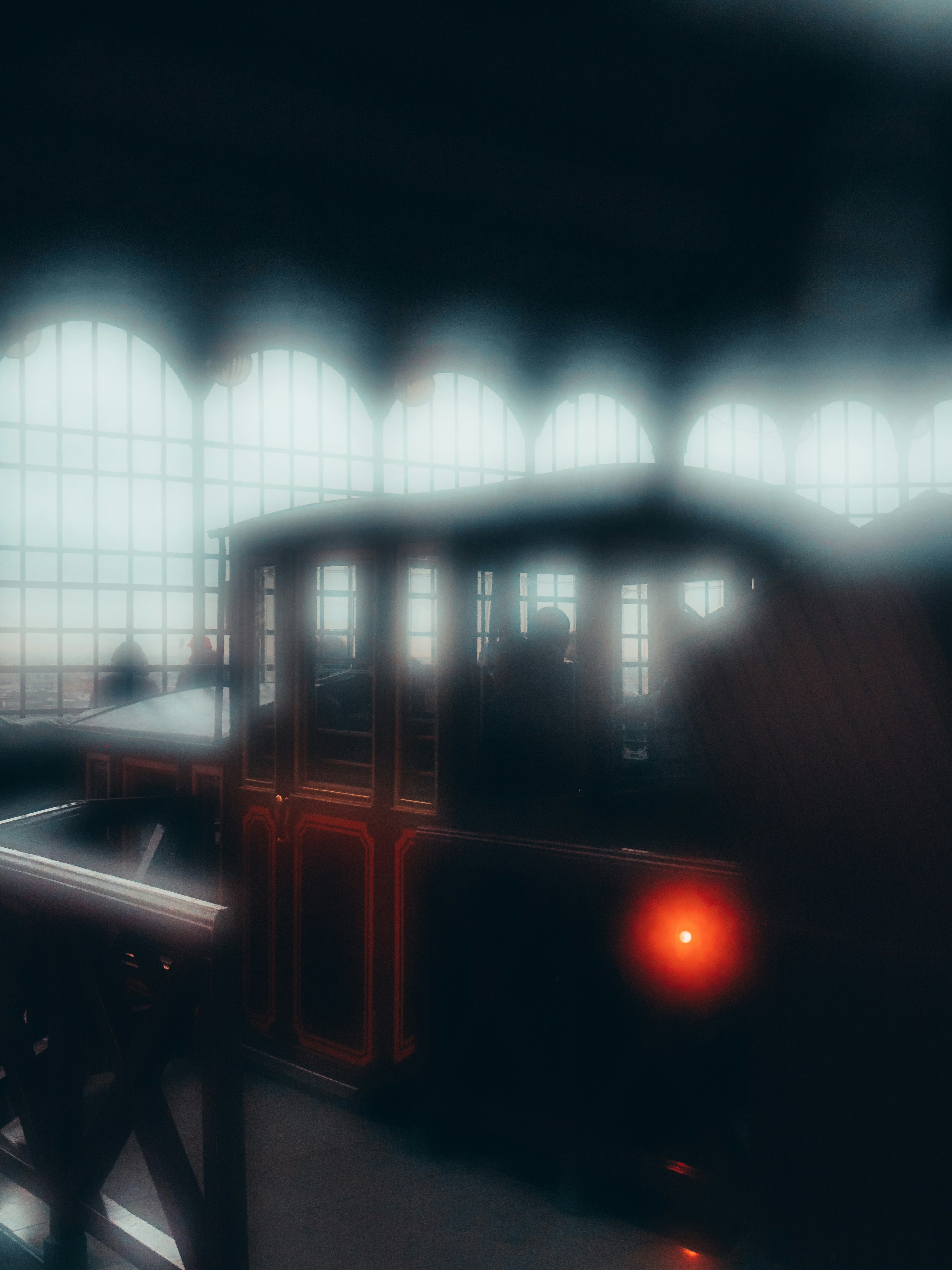 A vintage train with a glowing red light sits inside an old station, framed by large arched windows that filter soft light.