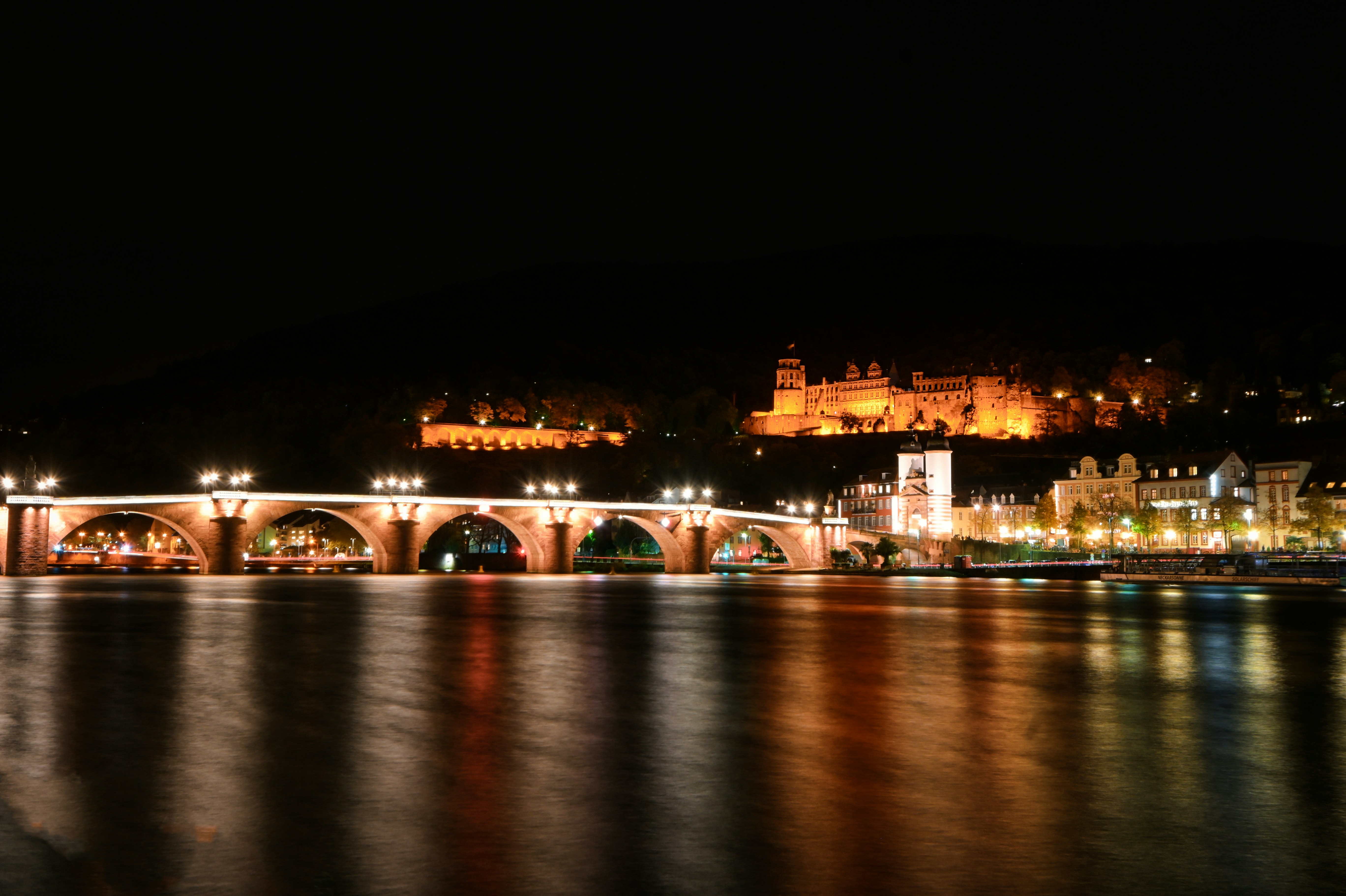 Historic bridge and hillside castle glowing against the night sky, with reflections on the river.