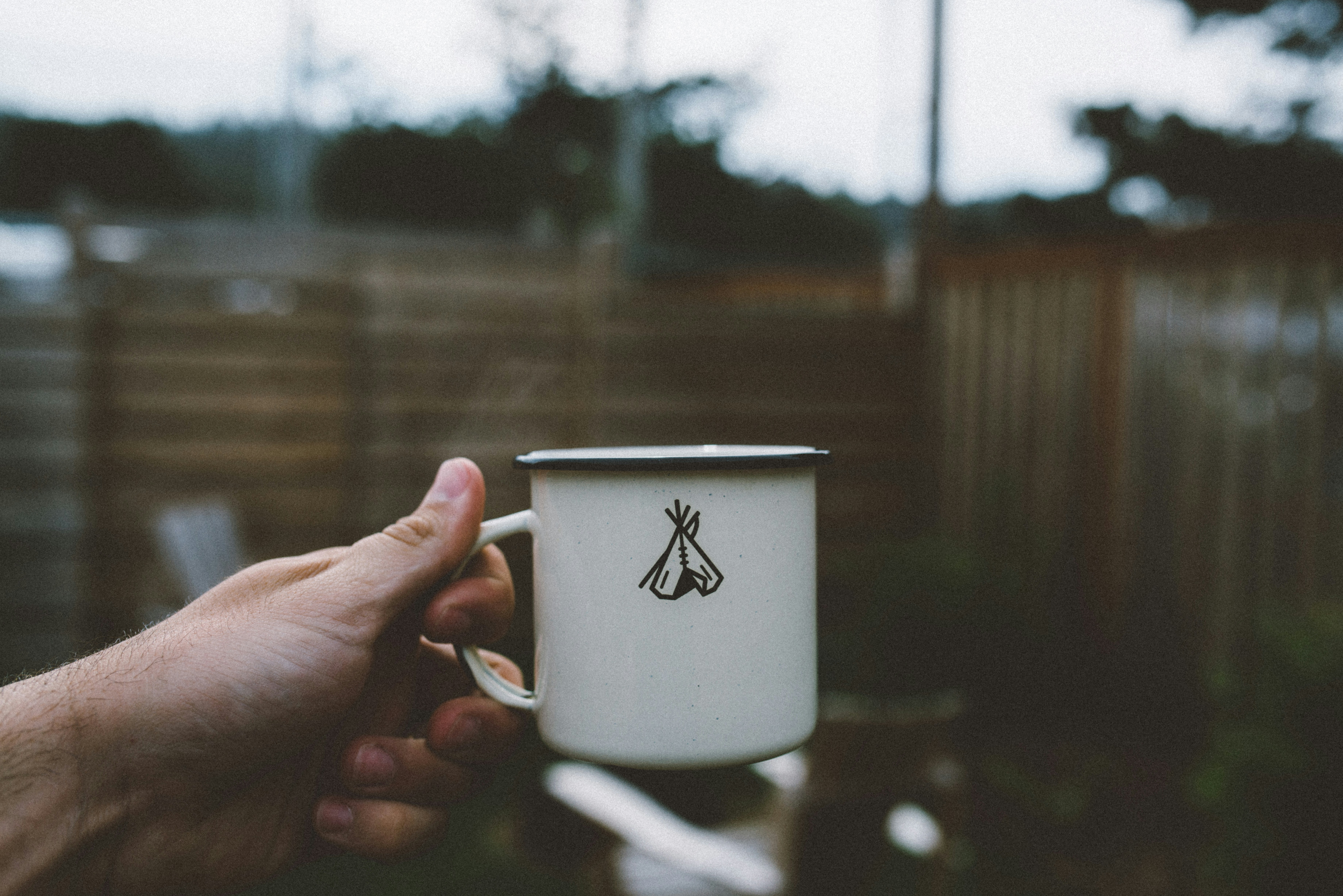 Morning Grip: An Enamel Mug Framed by a Faded Fence