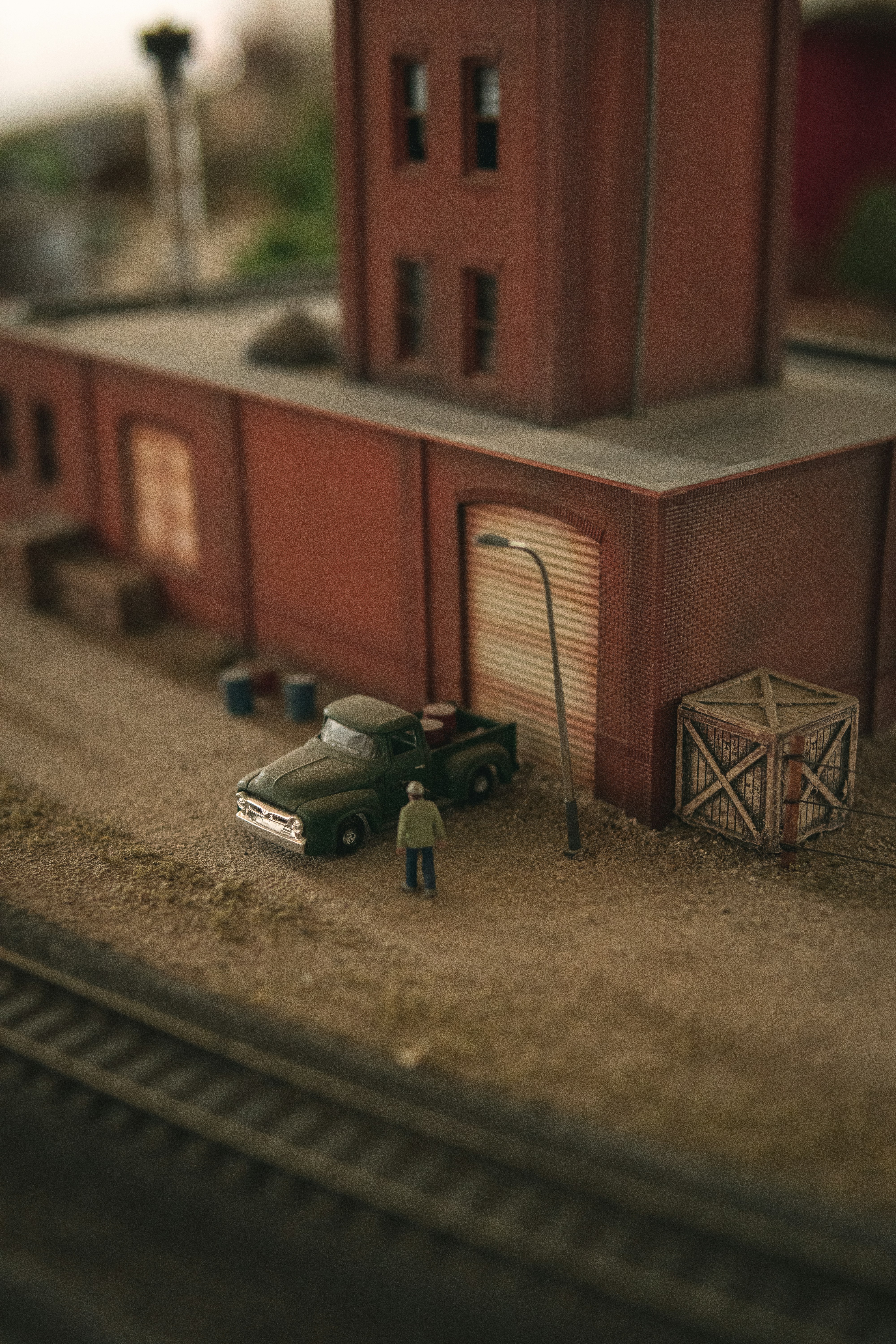 Model scene featuring a small figure beside a vintage truck in front of a brick building, capturing the essence of a bustling industrial setting.