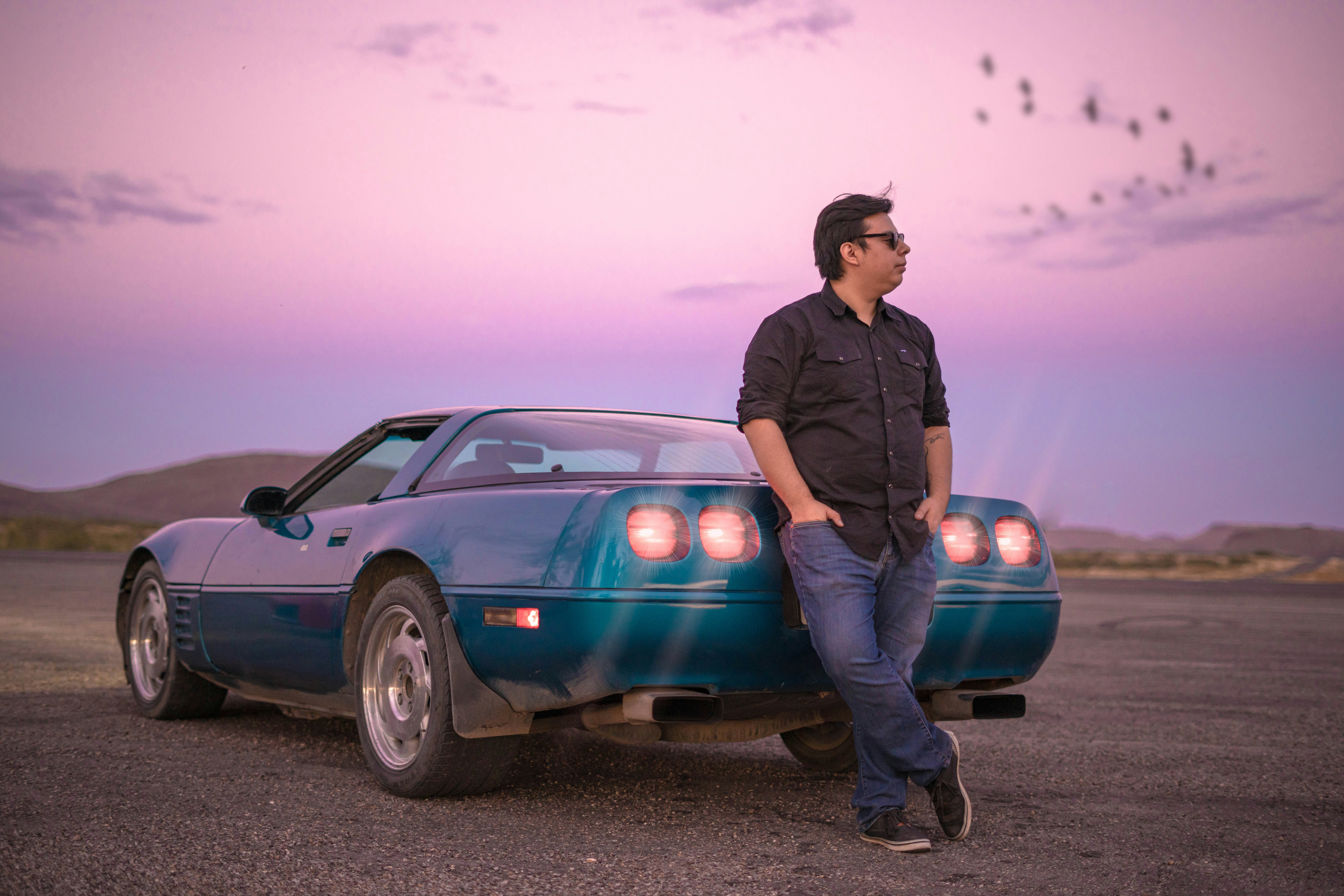 a man leaning on the hood of a blue sports car