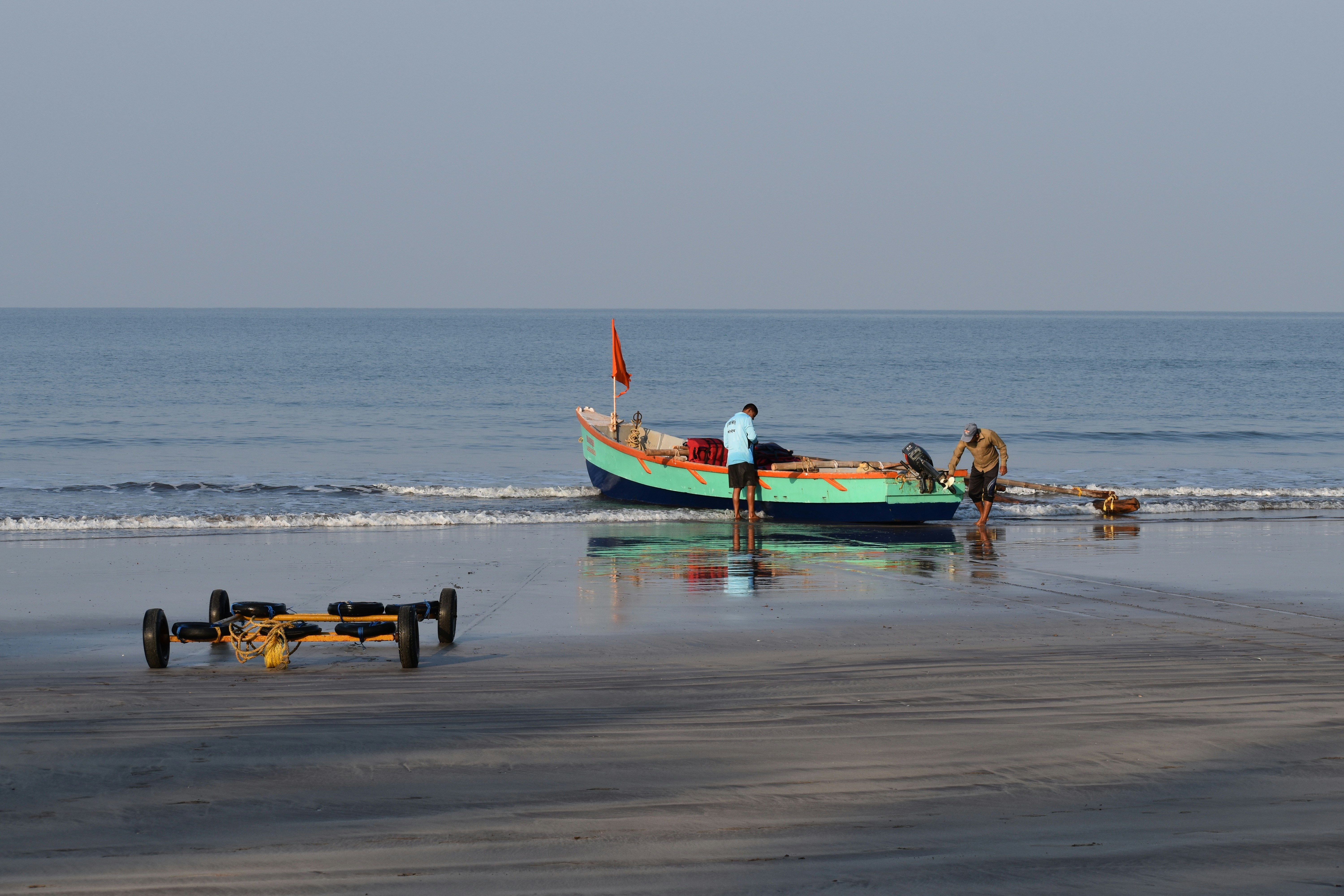 Fishermen preparing their colorful boat on a tranquil beach, with gentle waves lapping at the shore. The scene captures the essence of coastal life.