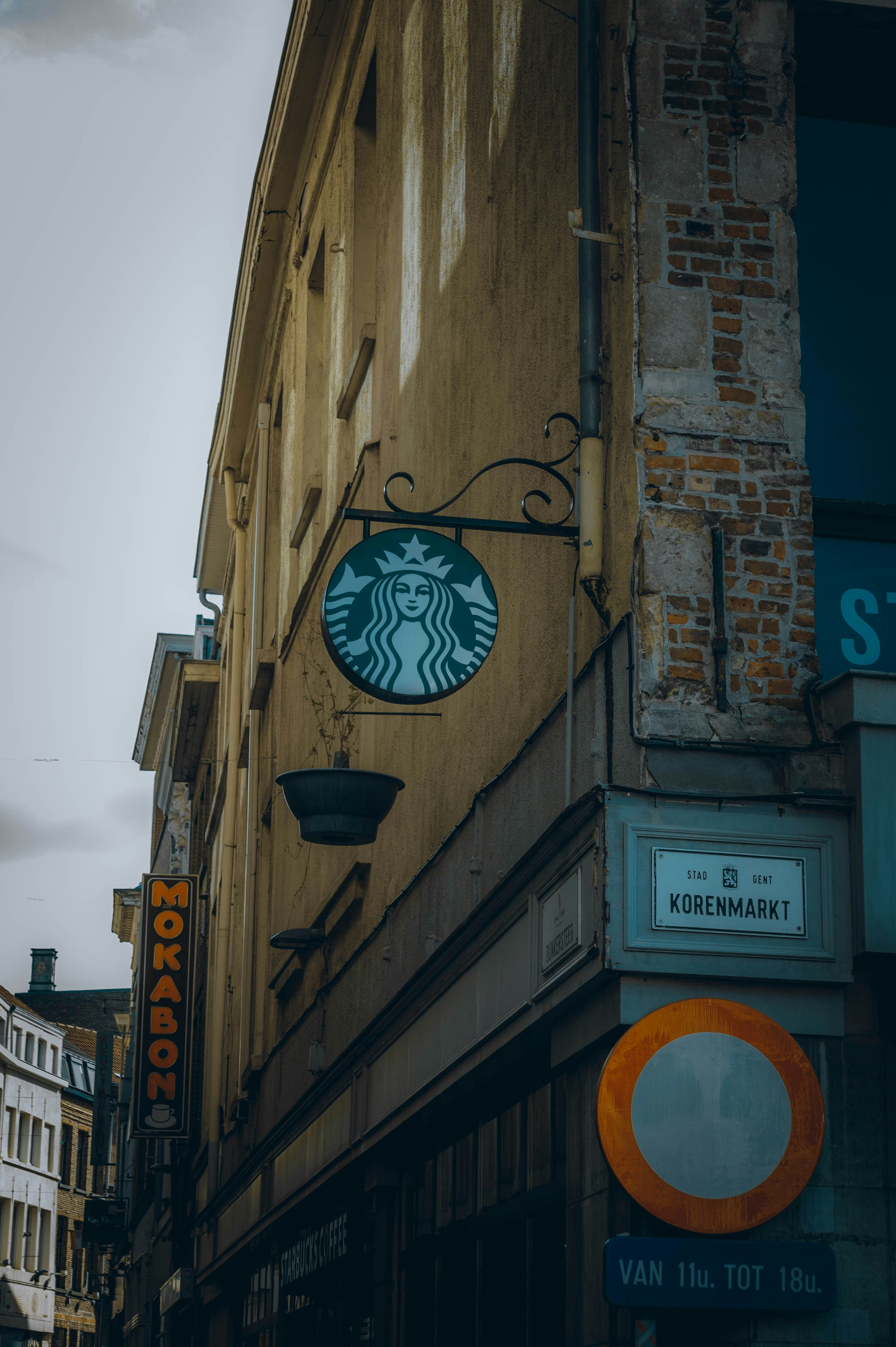 Starbucks logo hanging on a vintage building corner, with nearby street signs and a warm ambiance. 