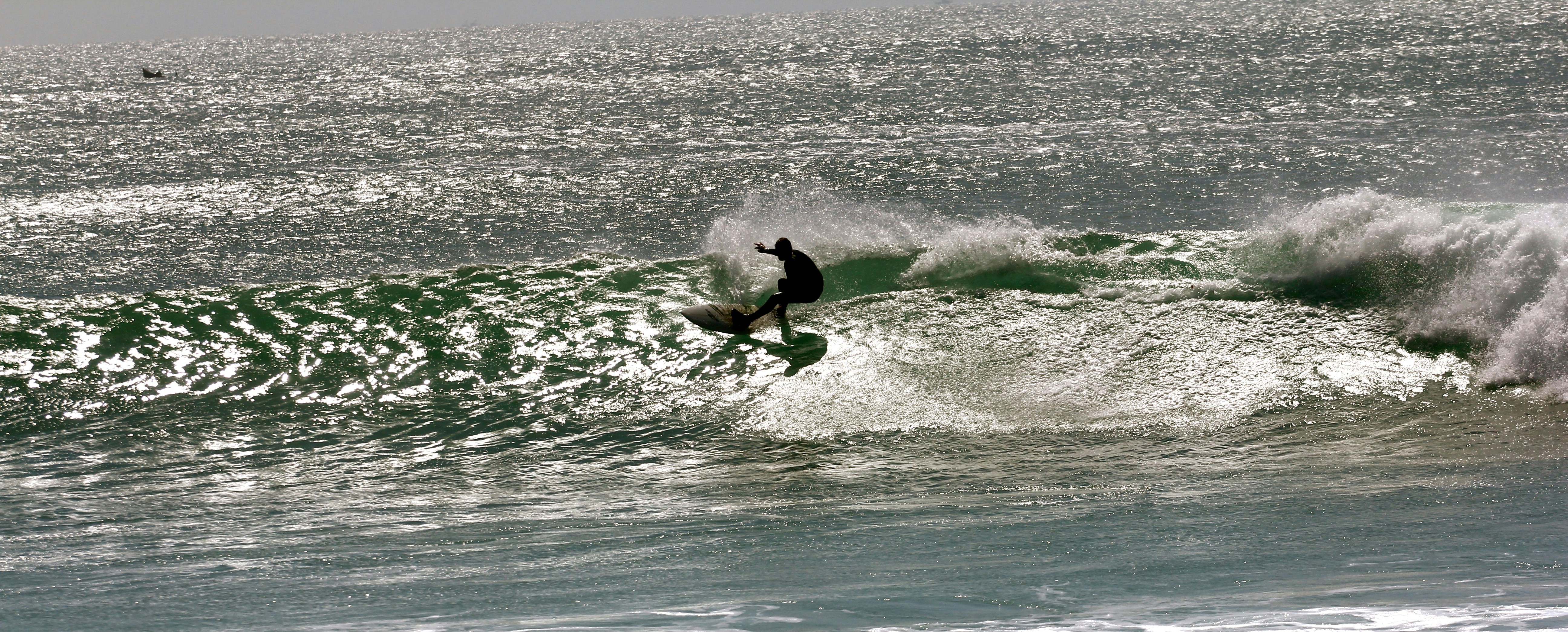 Surfer carving through a shimmering wave under a bright sky, showcasing the dynamic energy of ocean sports.