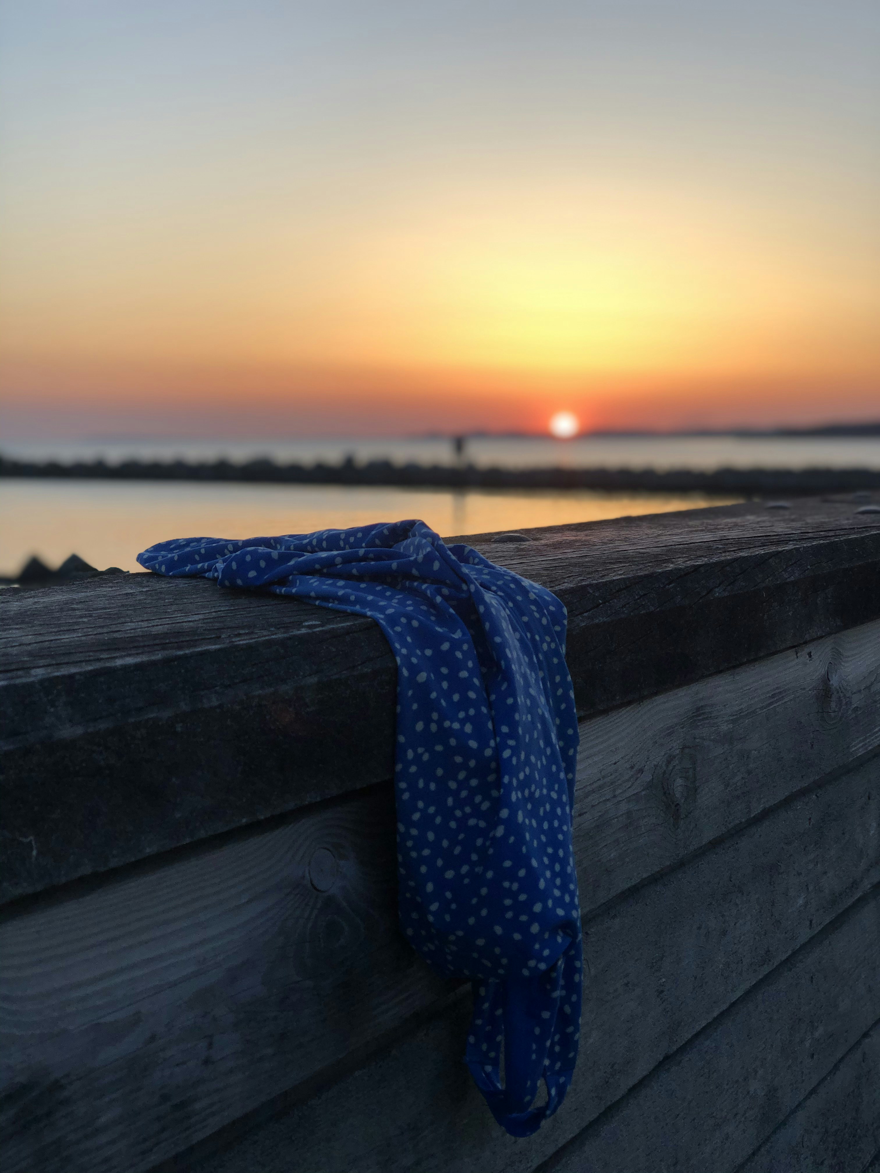 Blue scarf draped over a weathered railing at sunset by a calm water