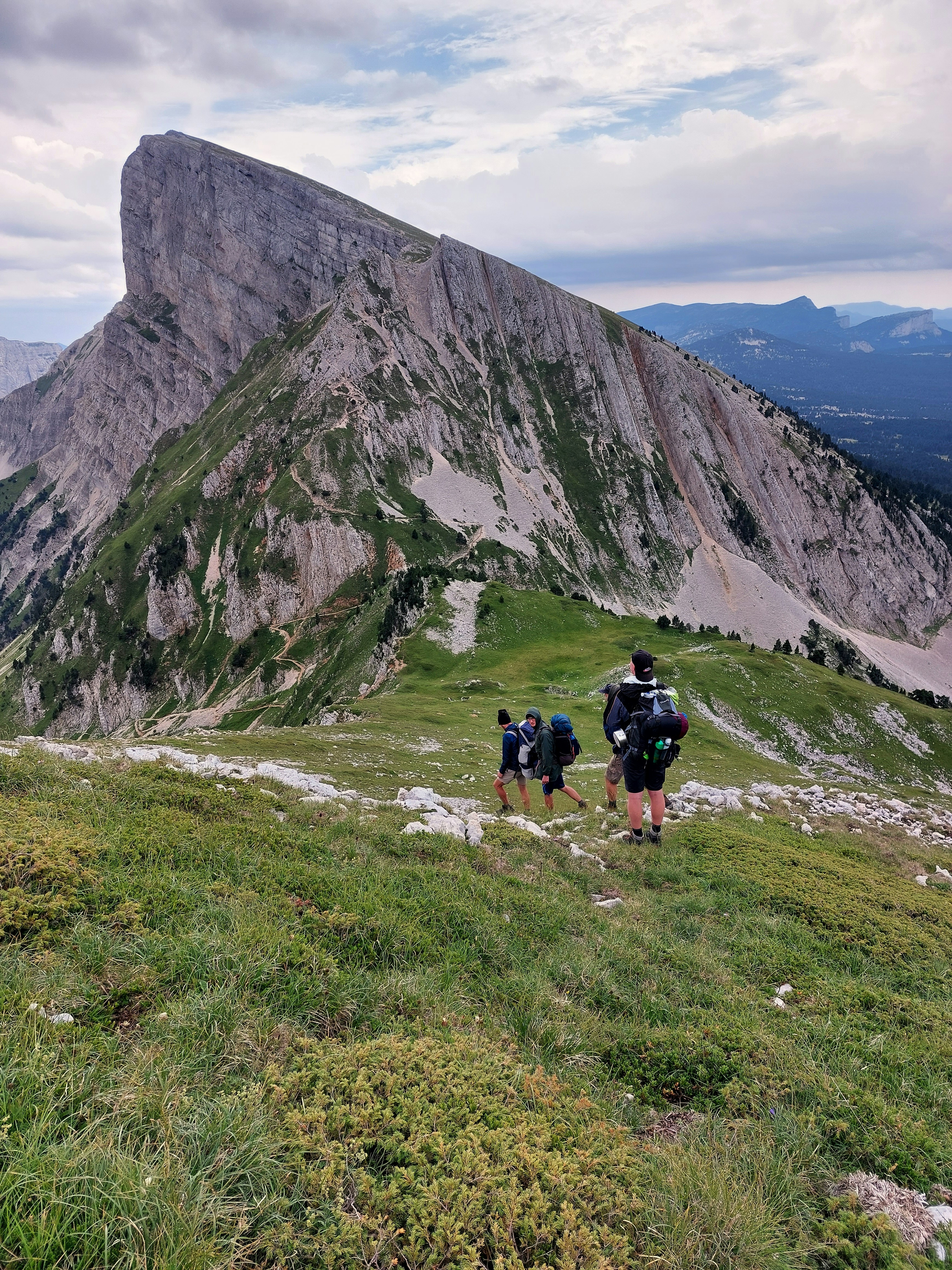 Alpine Ascent Toward a Granite Sentinel: Four Hikers on a Green Spine