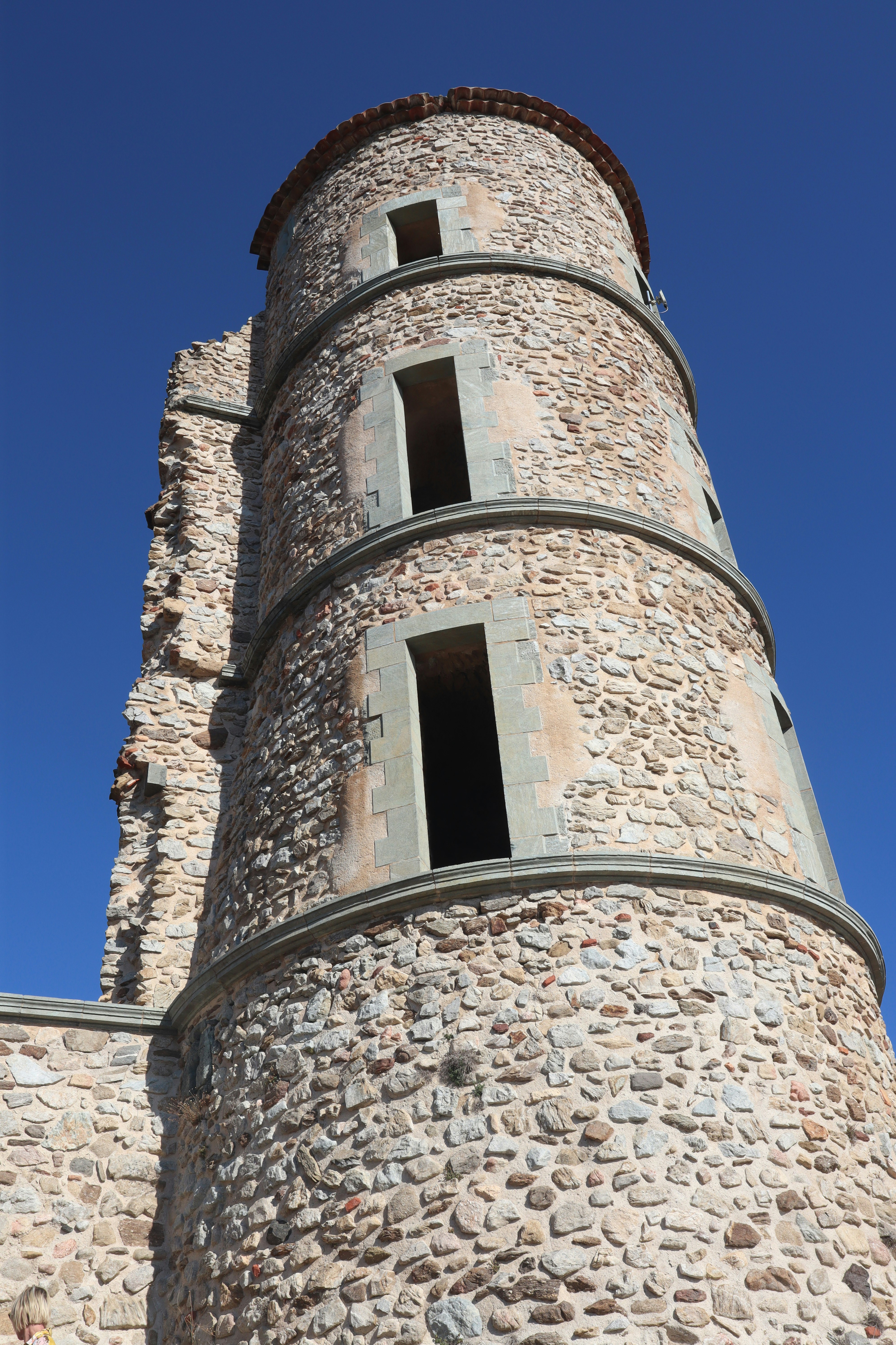 Ancient stone tower rising against a clear blue sky, showcasing its weathered texture and architectural details.