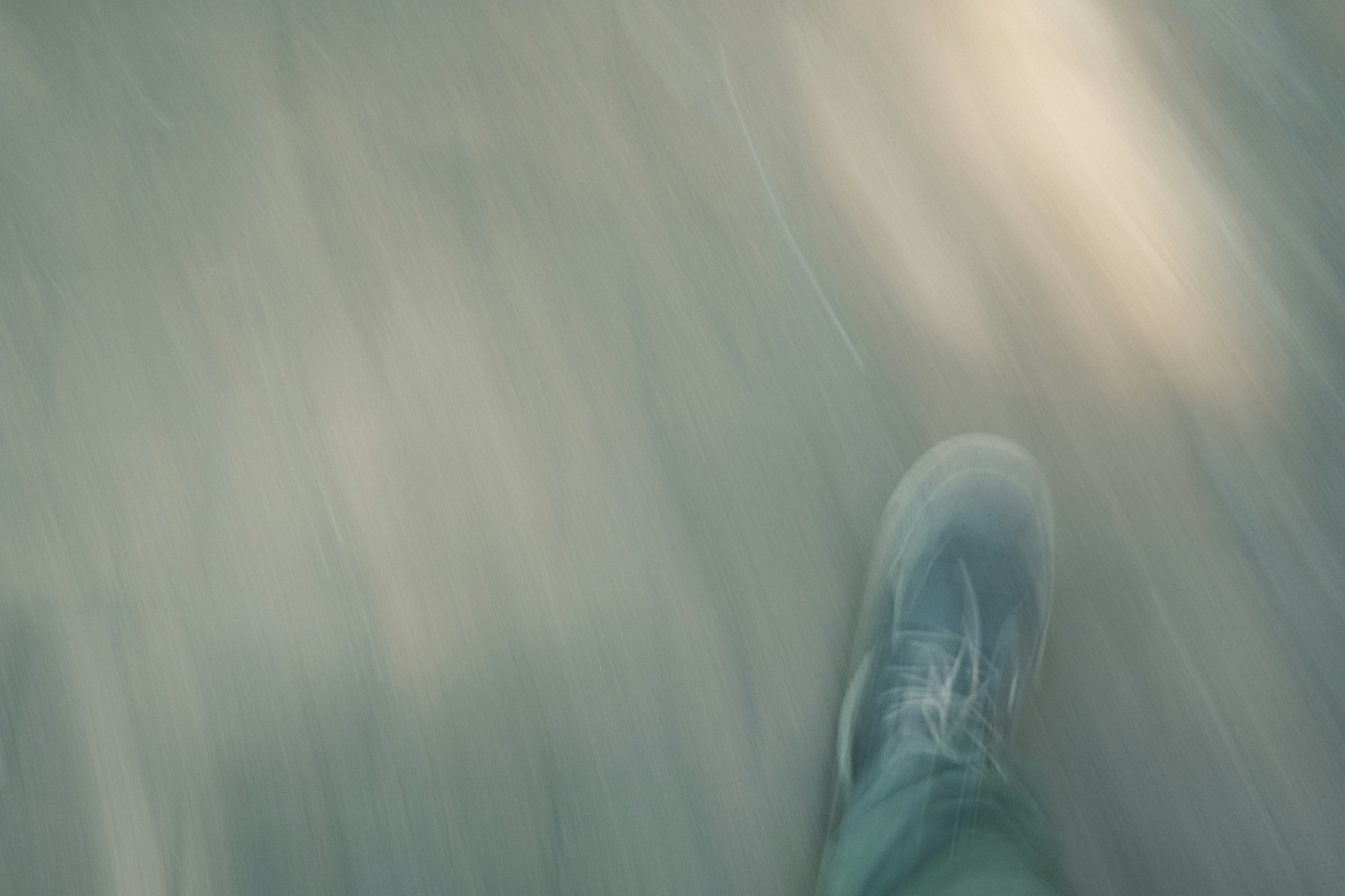 Foot stepping on a blurred path, evoking a sense of movement and exploration. The soft colors and motion create an immersive experience.