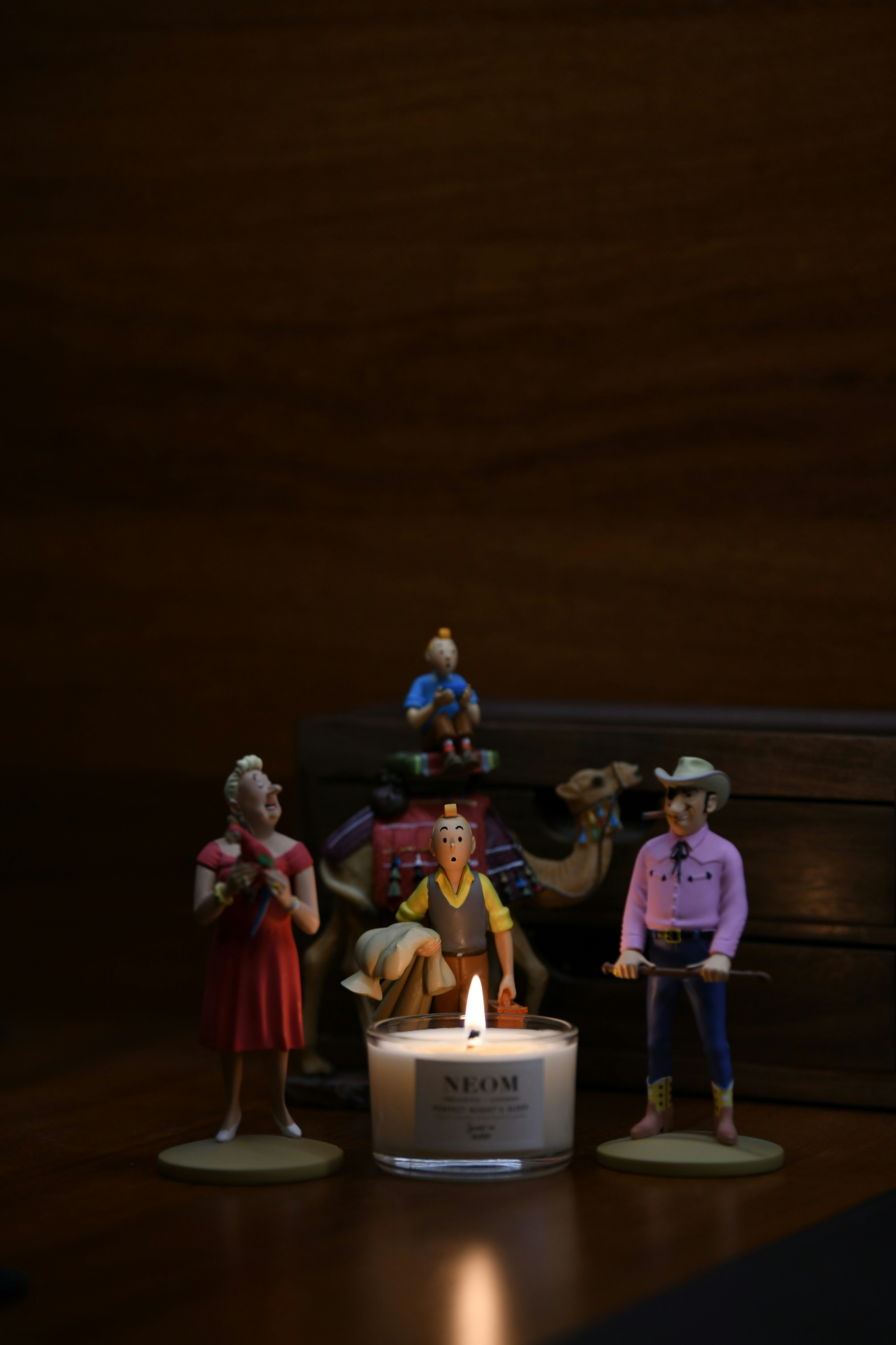 Three colorful figurines stand around a glowing candle on a wooden surface, creating a warm and inviting atmosphere.
