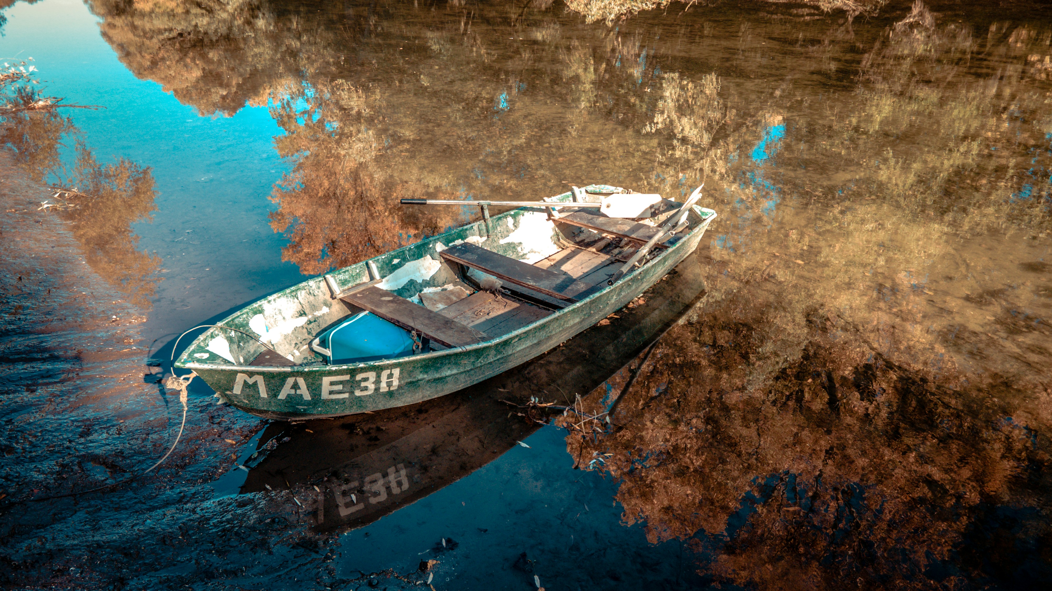 An old green boat rests peacefully on calm waters, reflecting the surrounding trees and sky. The tranquil scene evokes a sense of nostalgia.