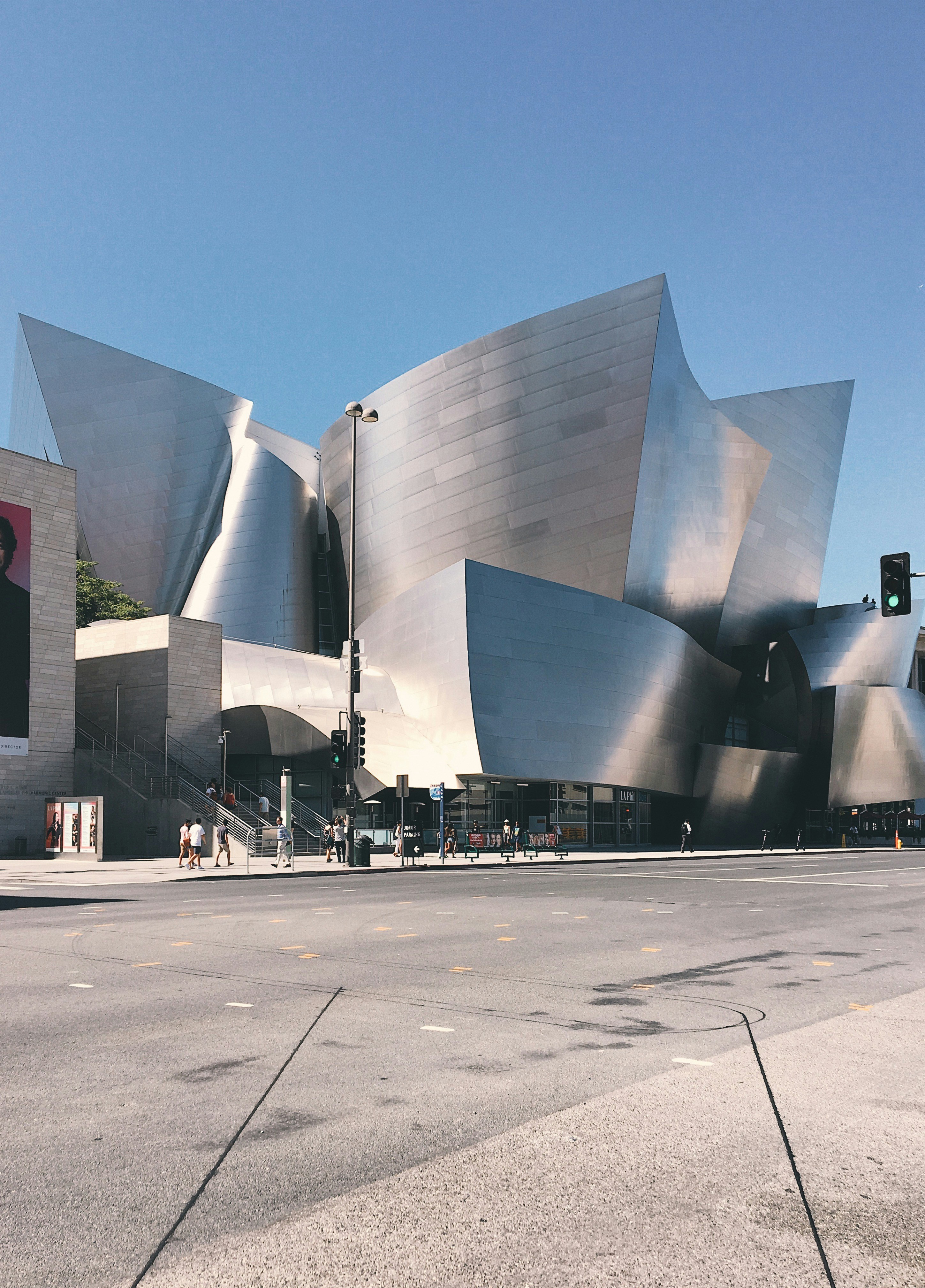Dynamic metallic structure showcasing contemporary architectural design with angular forms and reflective surfaces. Pedestrians navigate the urban landscape around it.