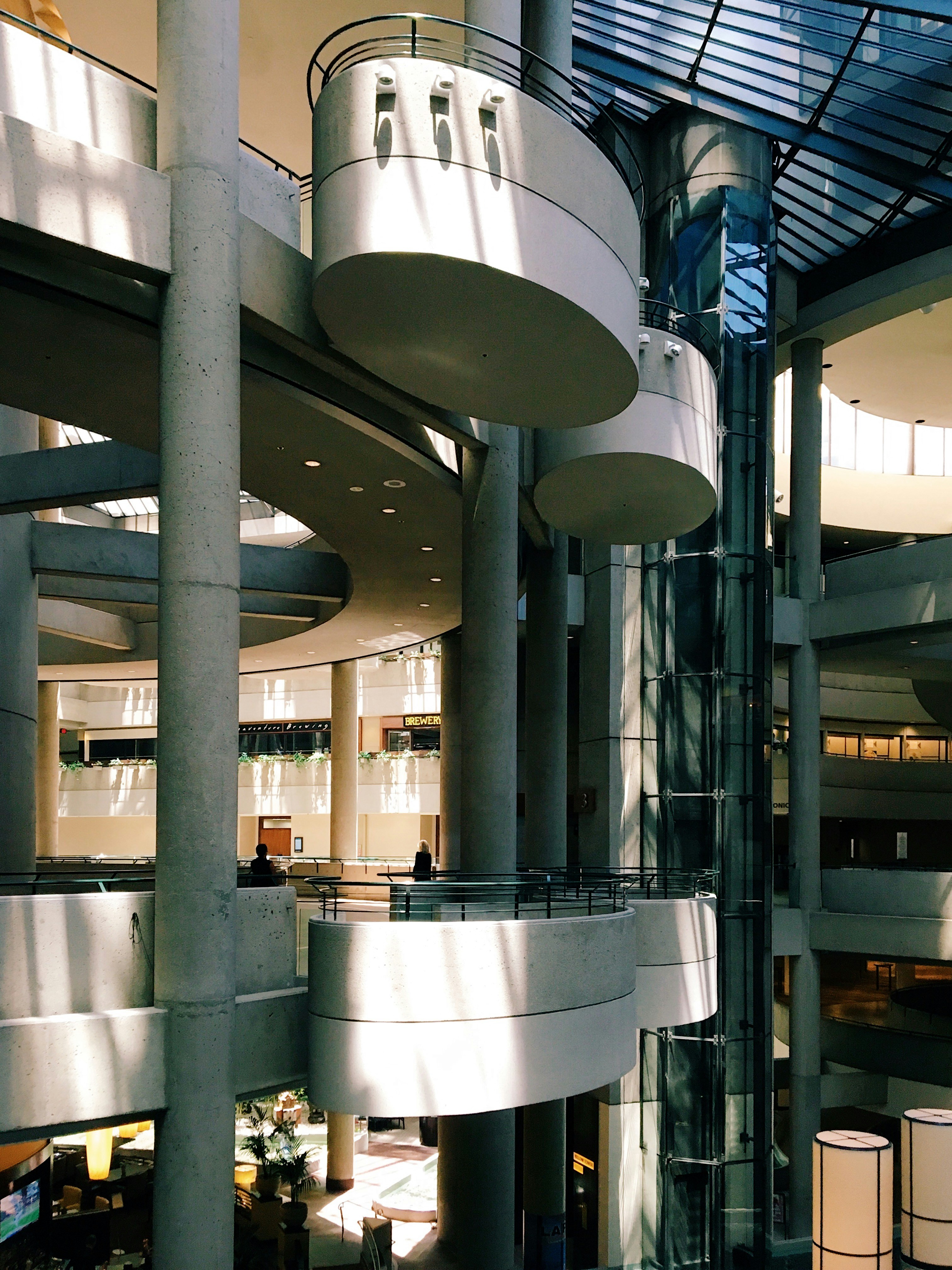 Modern interior showcasing curved balconies and pillars, illuminated by natural light streaming through the glass ceiling.