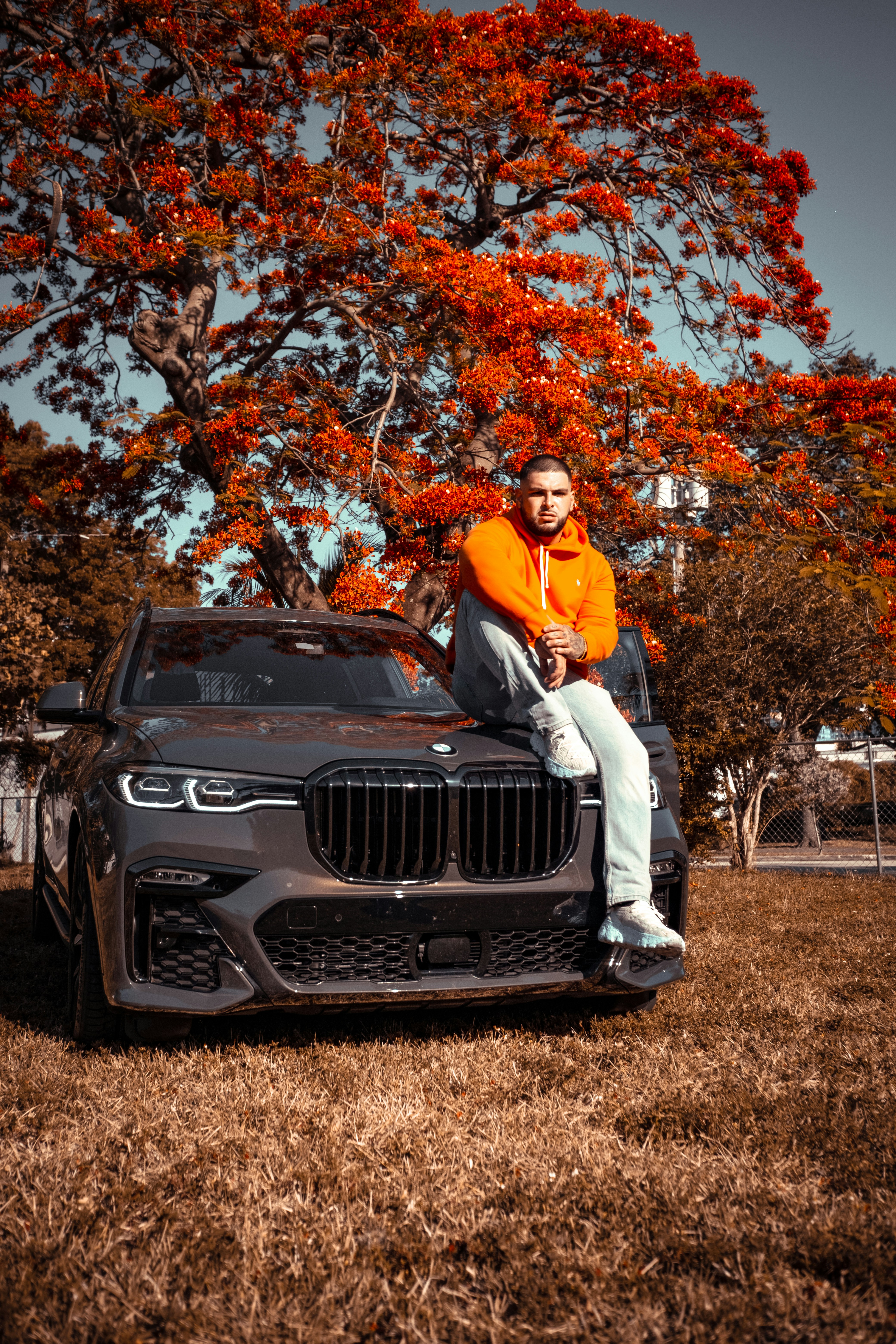 Orange hoodie, chrome grille: a rider perched on a BMW X6 in autumn light