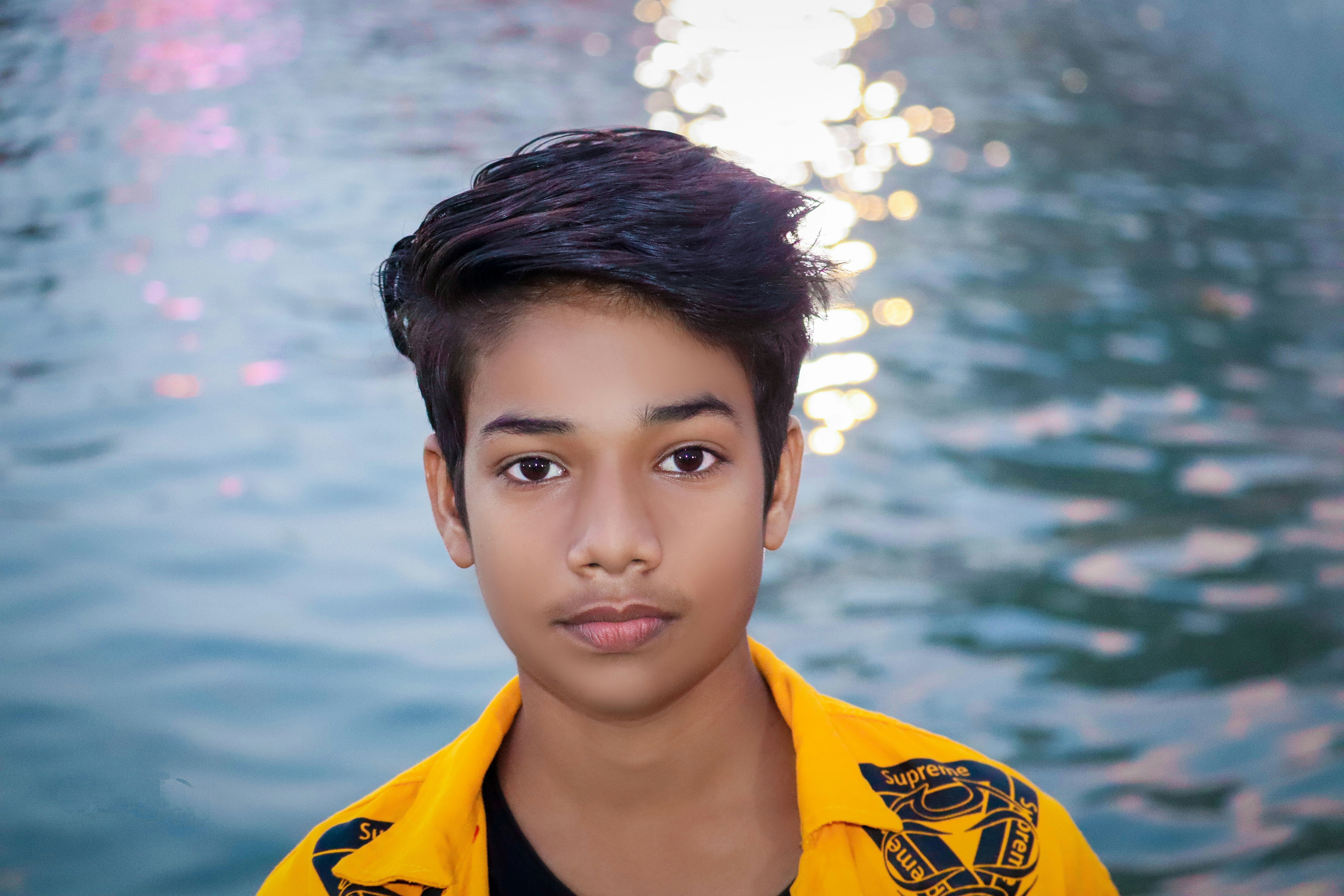 A boy with a yellow jacket standing in front of a body of water photo ...