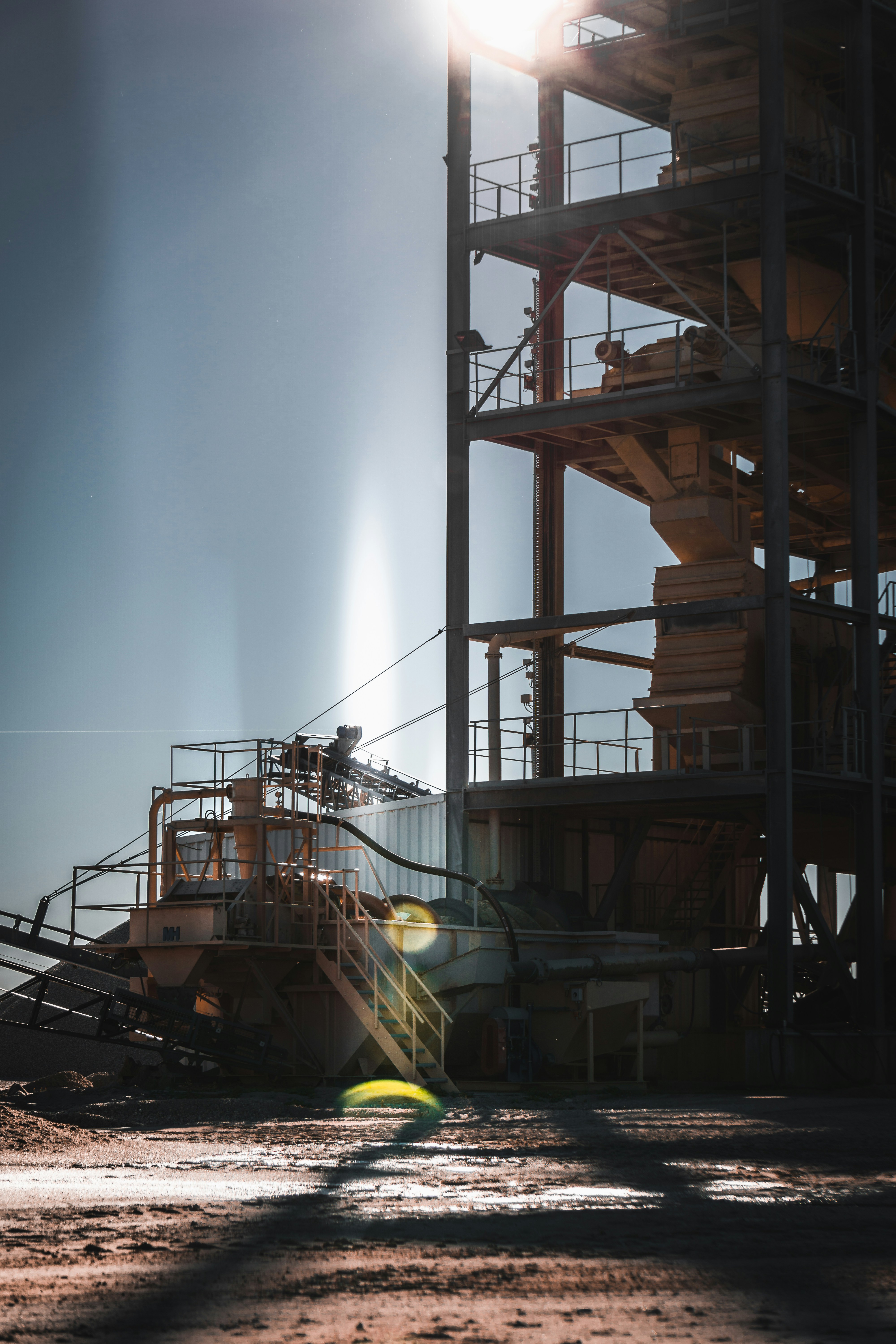 A towering industrial structure glistens under the sun, casting intricate shadows on the ground. The scene captures the harmony between machinery and natural light.