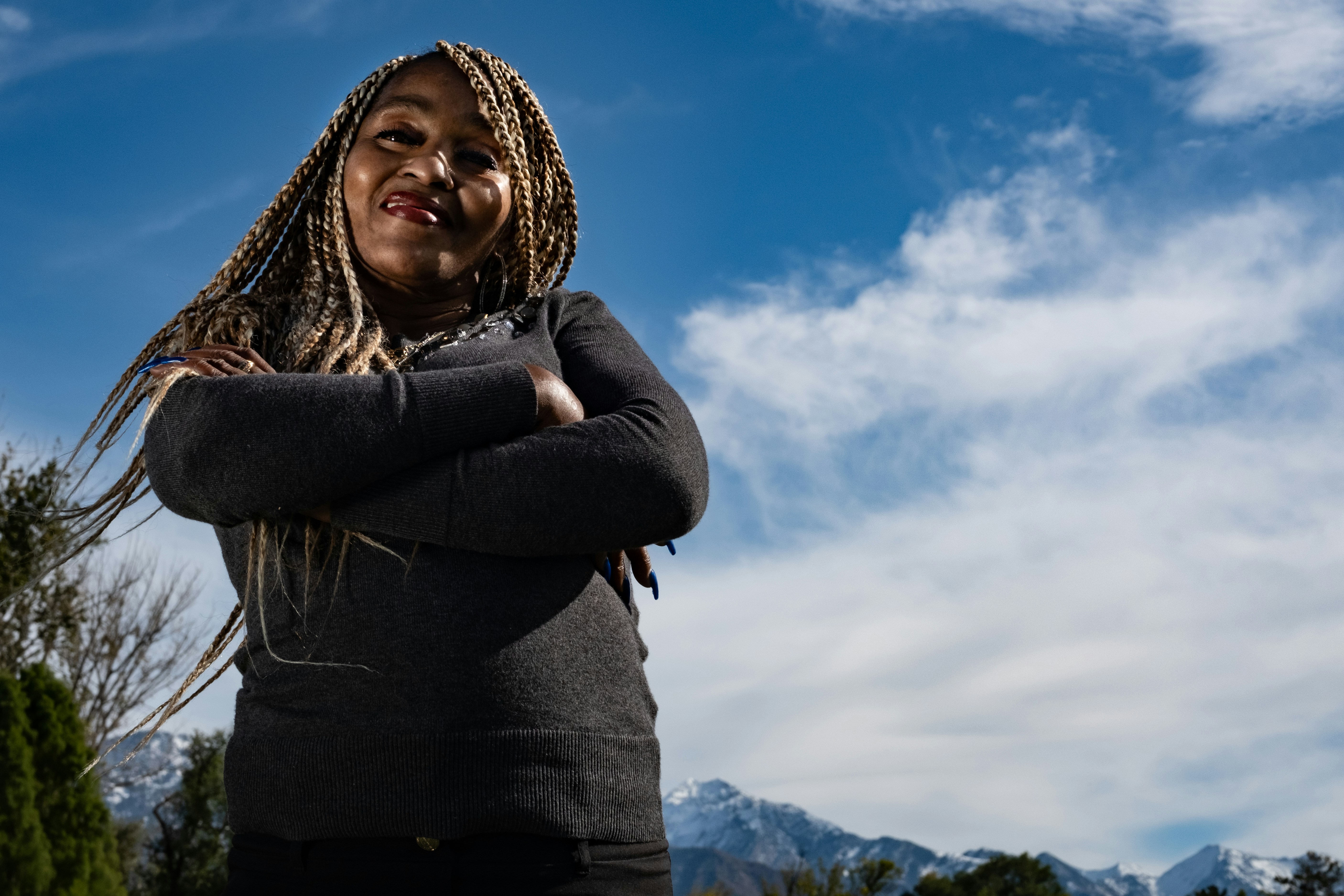 Powerful Black woman from low perspecting in front of clouds, blue sky, and mountains