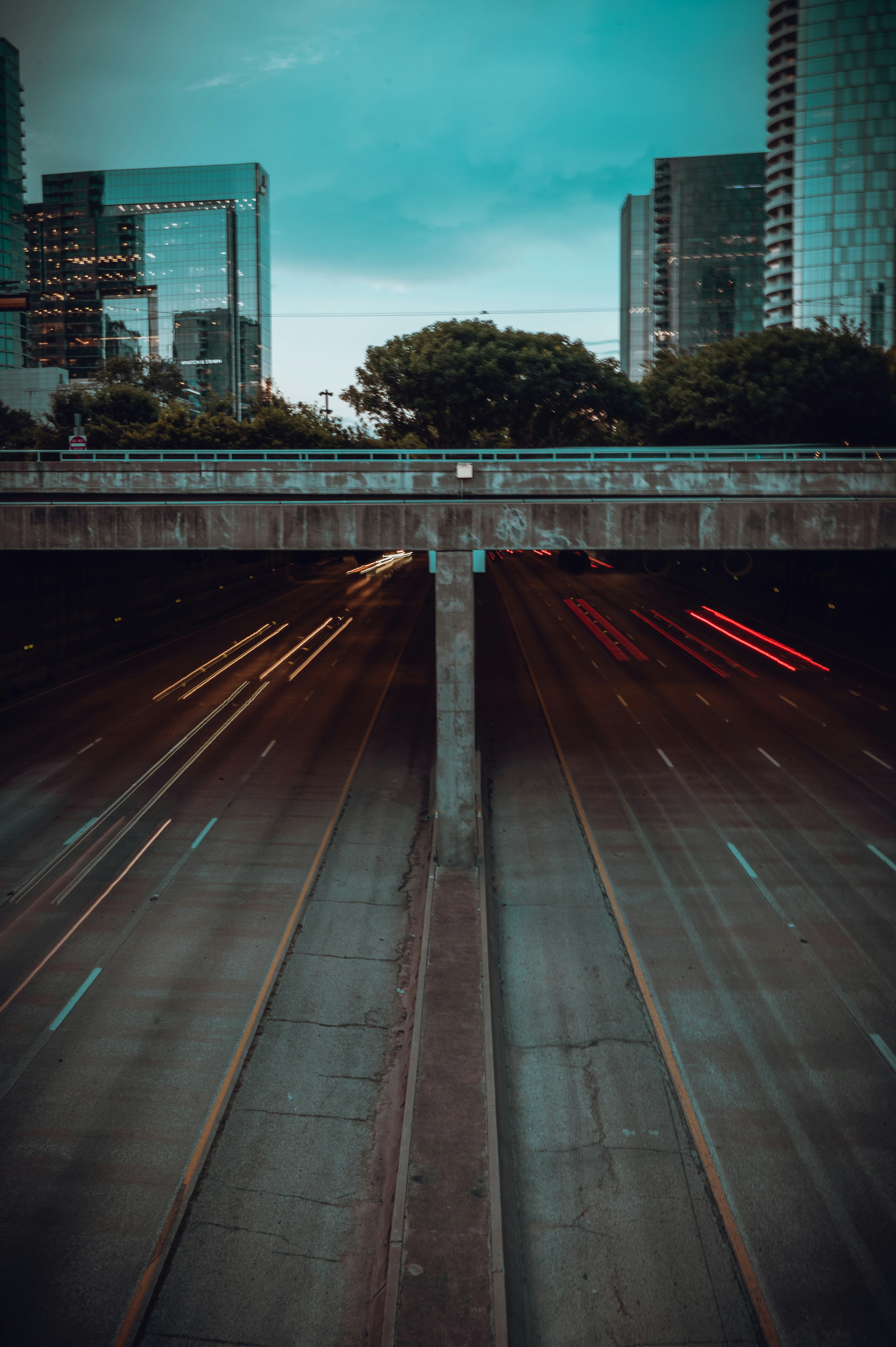 Long exposure shot capturing the dynamic flow of traffic beneath an overpass in a modern cityscape, with skyscrapers in the background.
