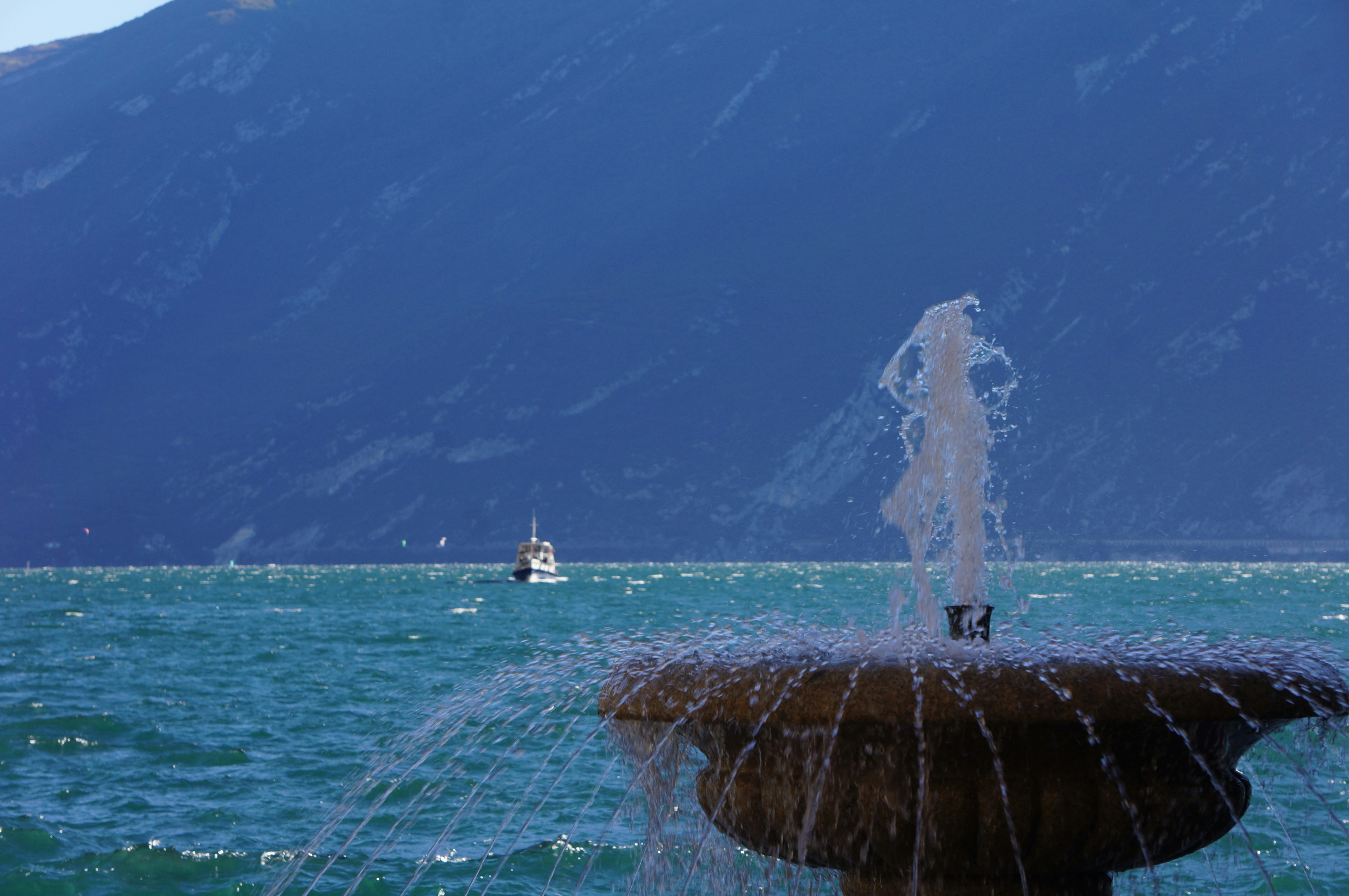 A fountain spewing water into the ocean with a boat in the background ...