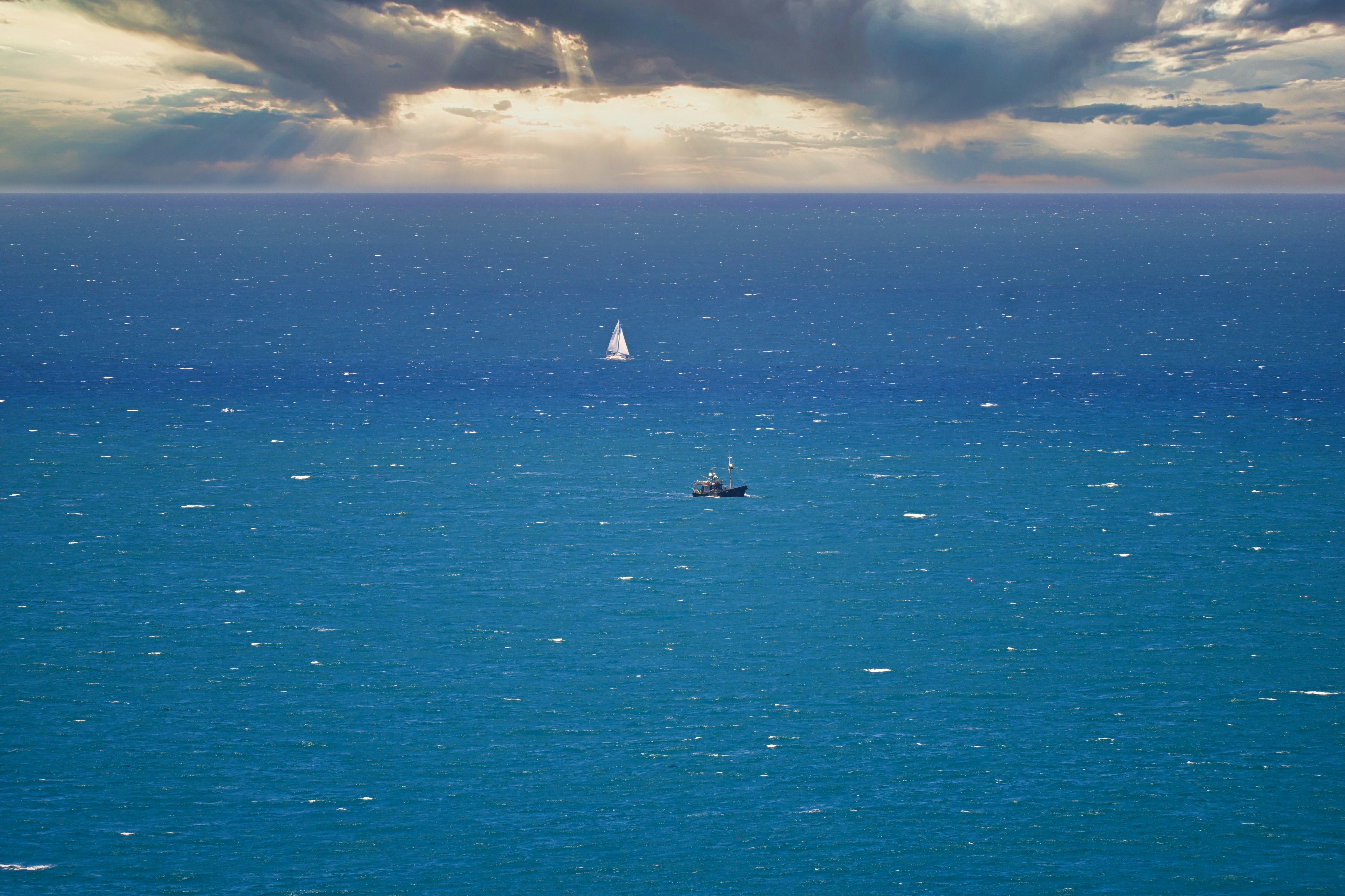 Lone Sailboat on a Cobalt Sea Beneath Narrow Sunbreaks