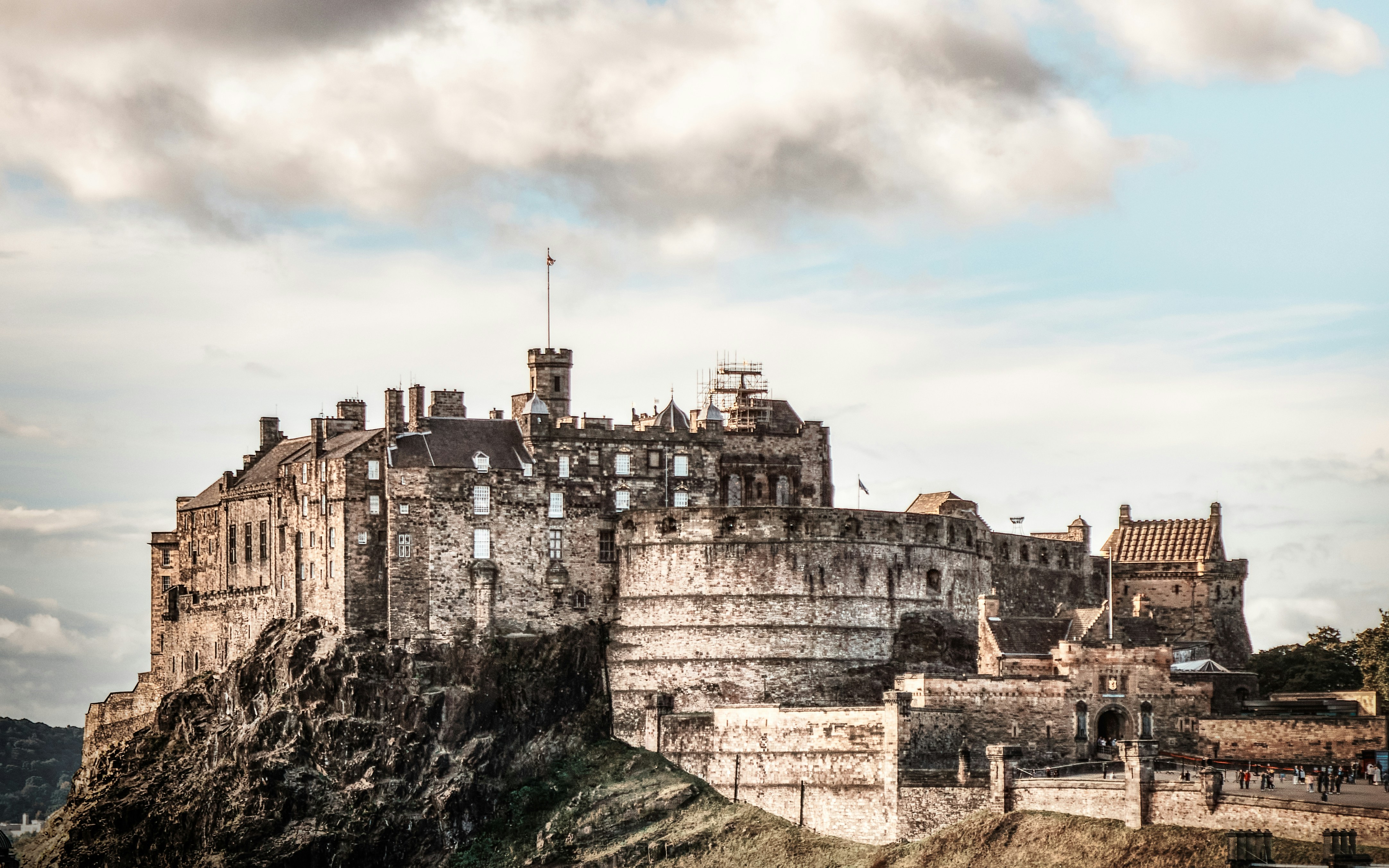 Historic stone castle perched on a rugged hill under a cloud-dappled sky.