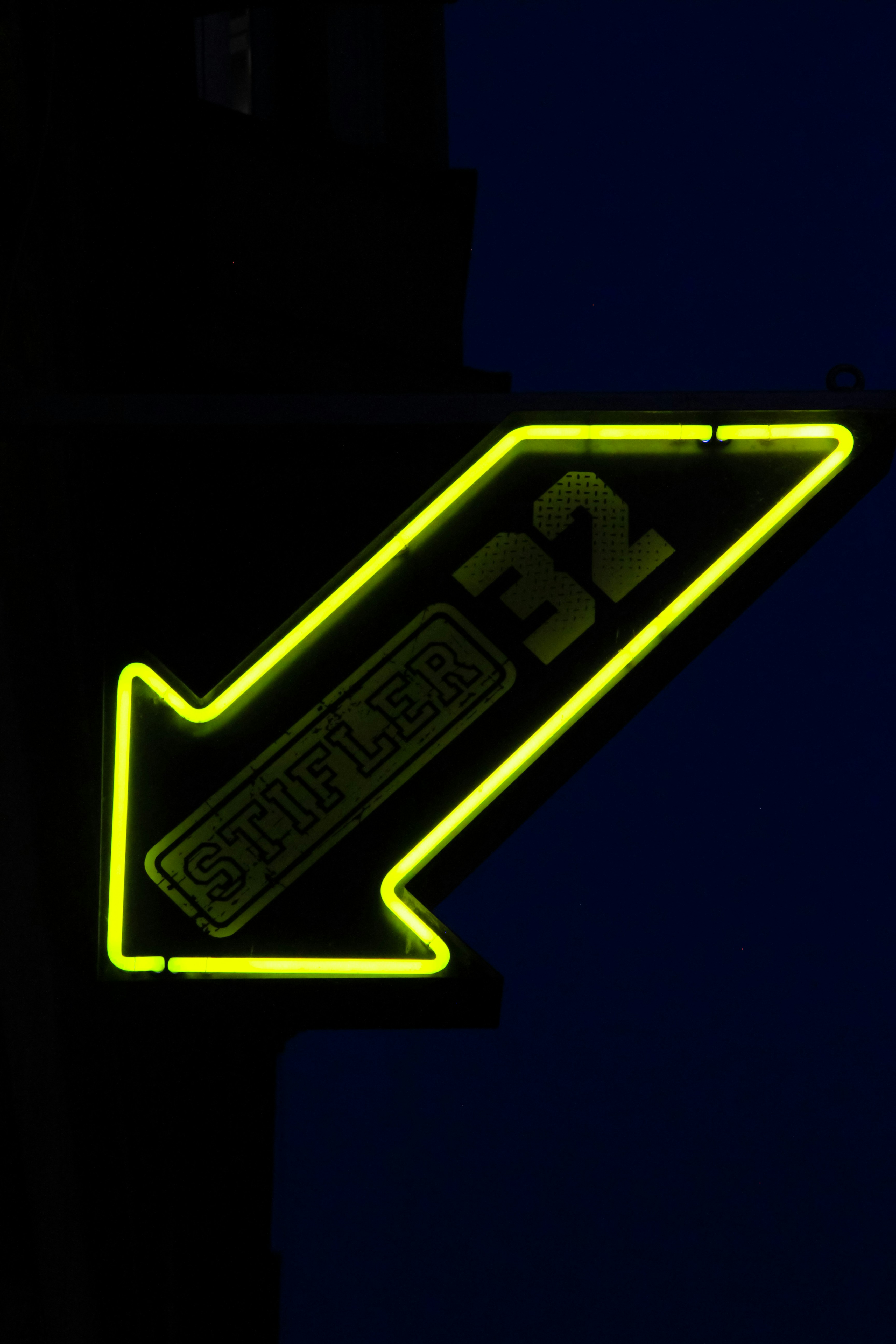 Illuminated neon sign featuring an arrow pointing left with the text 'STIFLER 32'.