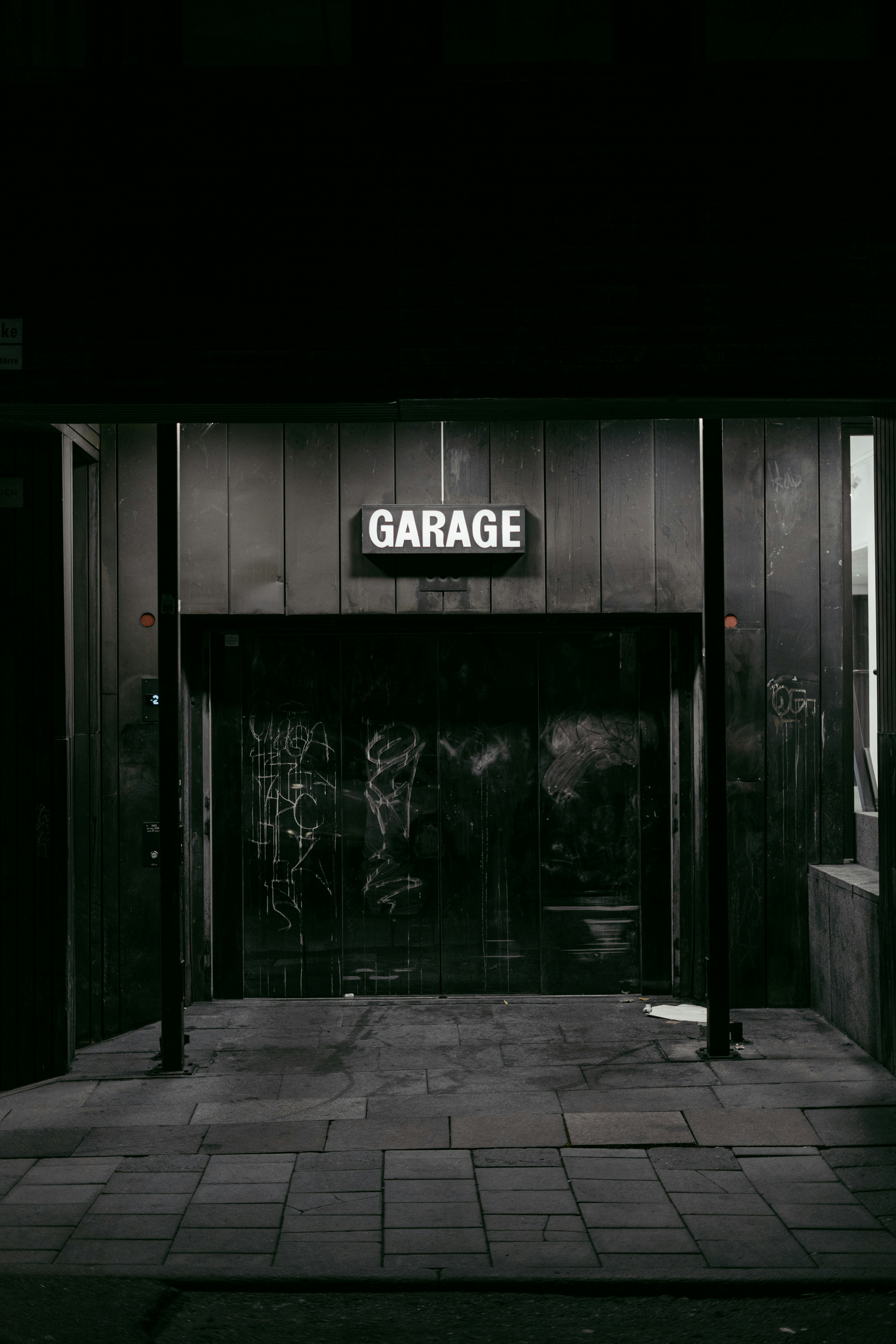 Dimly lit garage entrance with a prominent illuminated sign, showcasing urban textures and graffiti. The scene captures the essence of city nightlife.