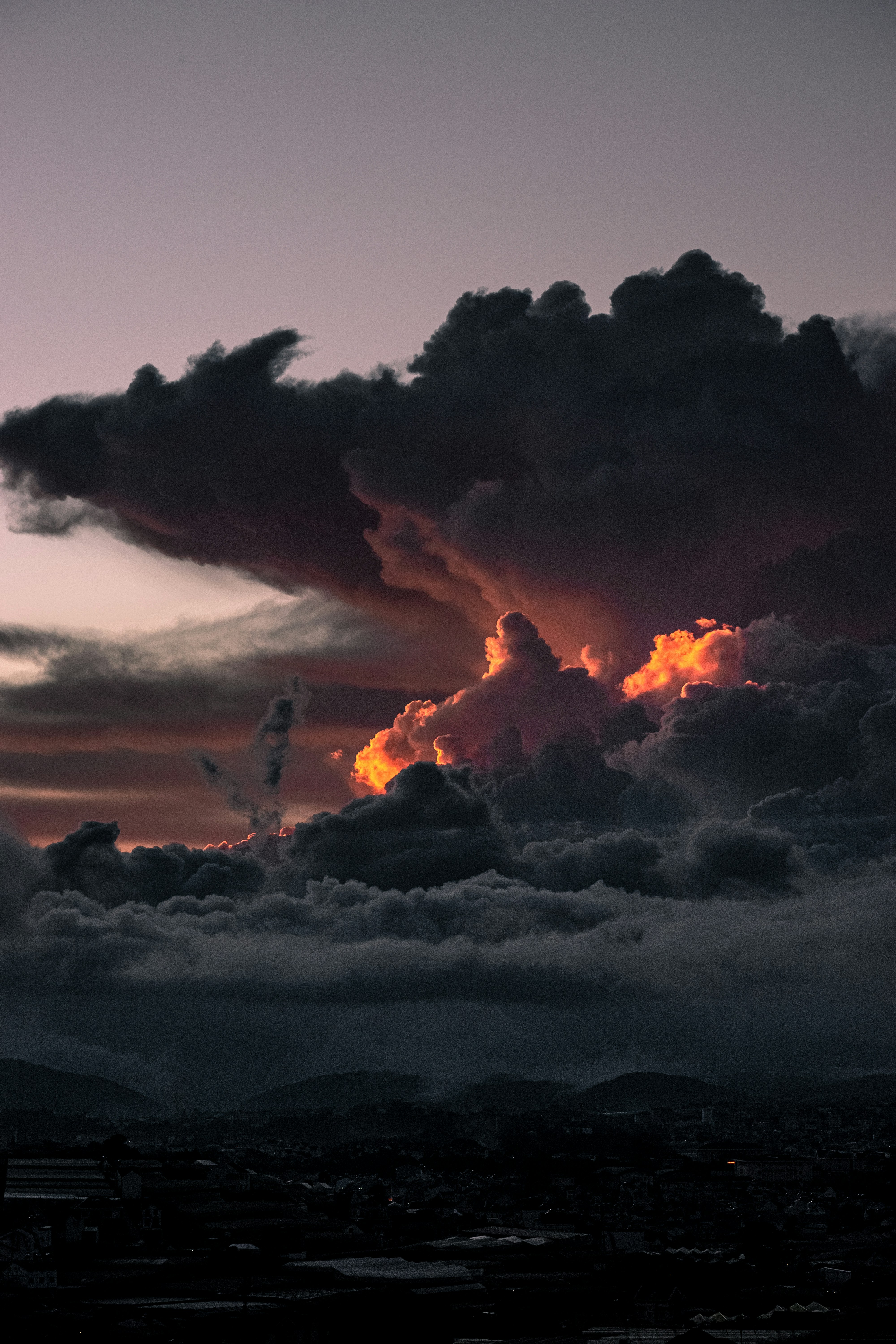 Dramatic clouds illuminated by a fiery sunset, showcasing a blend of colors and textures in the sky. The scene captures the dynamic interplay of light and shadow.