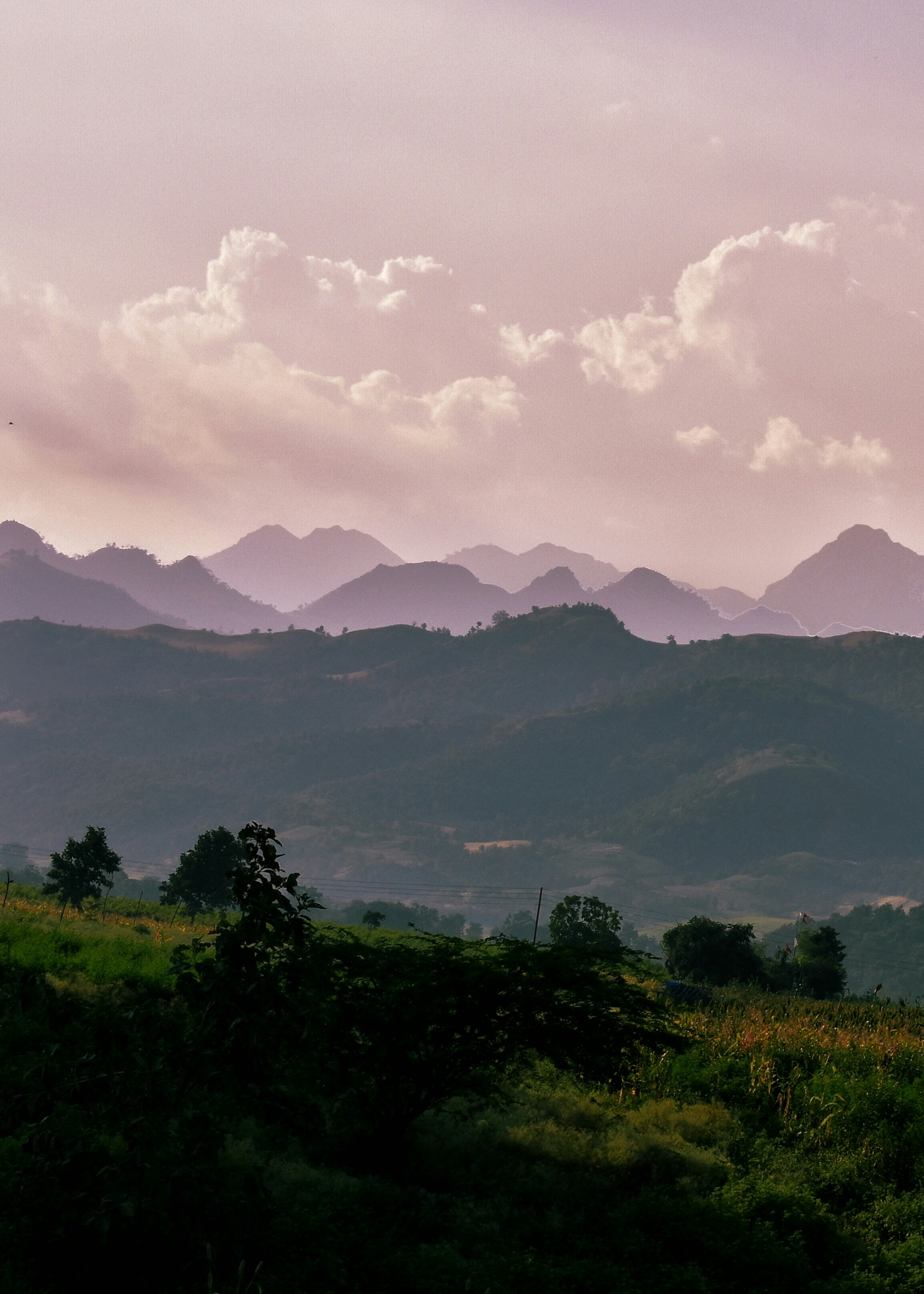Layered mountains under a soft pink sky with wispy clouds, showcasing the serene beauty of nature's contours.