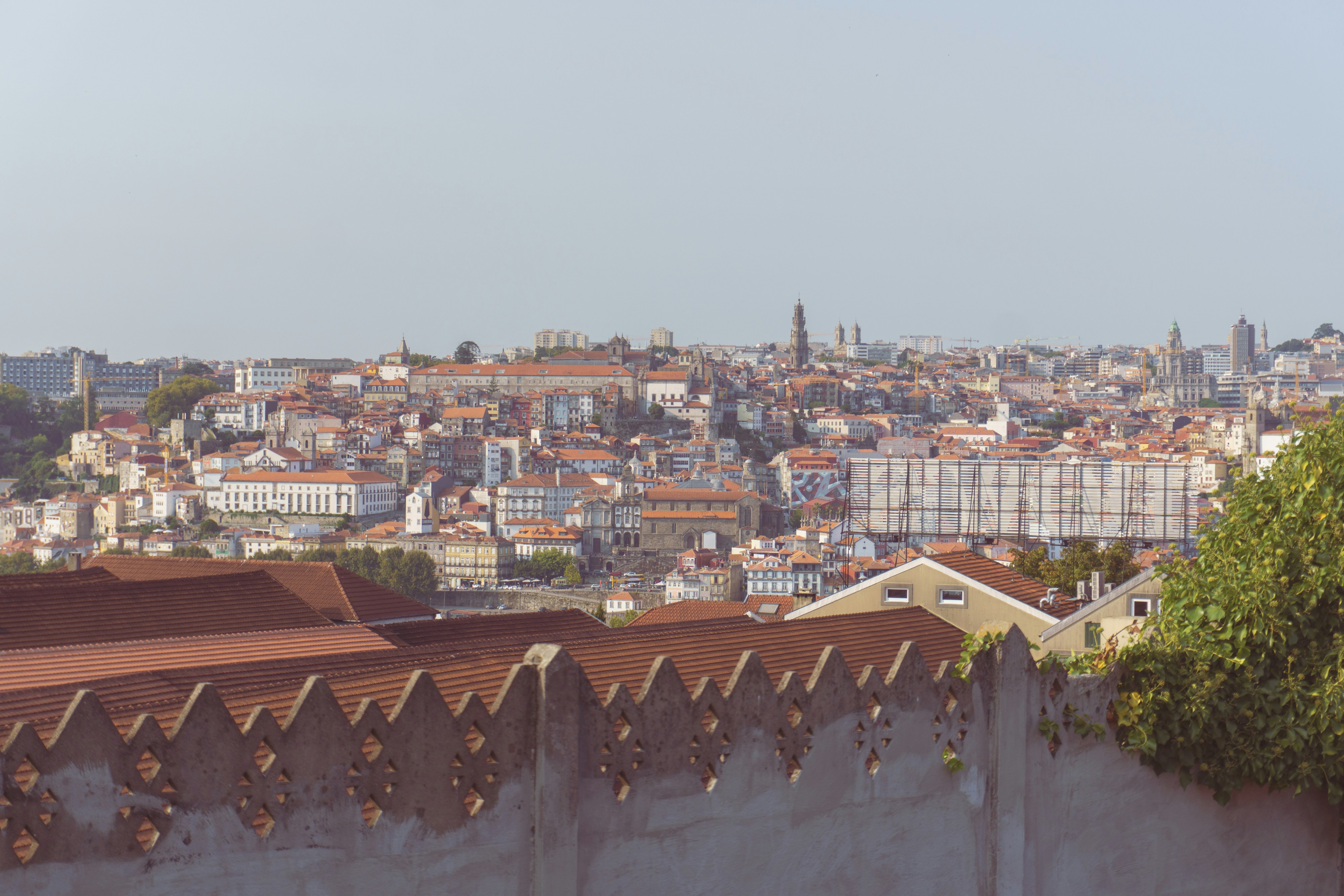 Panoramic view of a historic cityscape featuring terracotta rooftops and a skyline dotted with architectural highlights. The scene captures the essence of urban living amidst a backdrop of greenery.