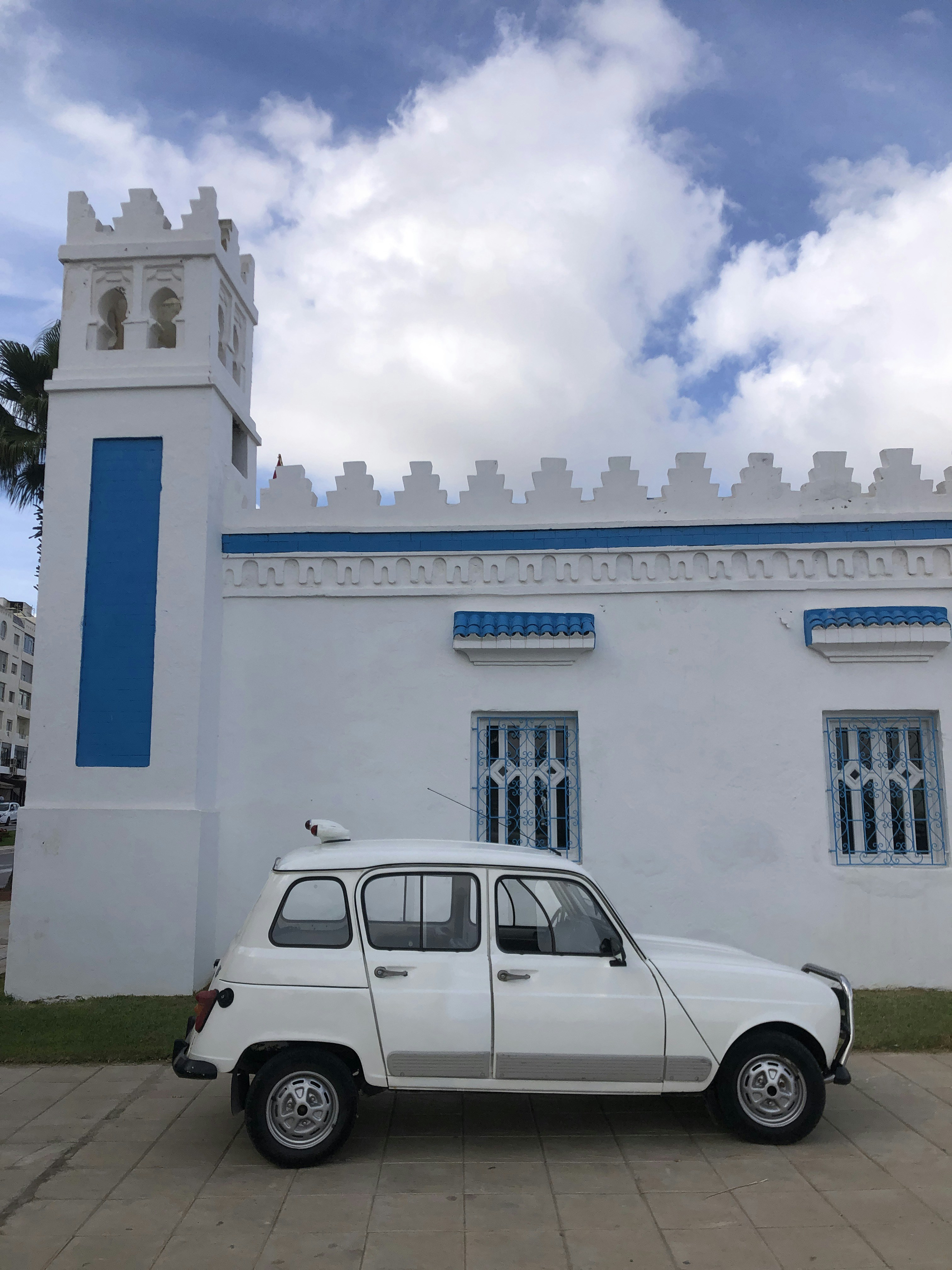A classic white car parked beside a striking blue and white building with decorative elements, showcasing a blend of vintage style and architectural beauty.