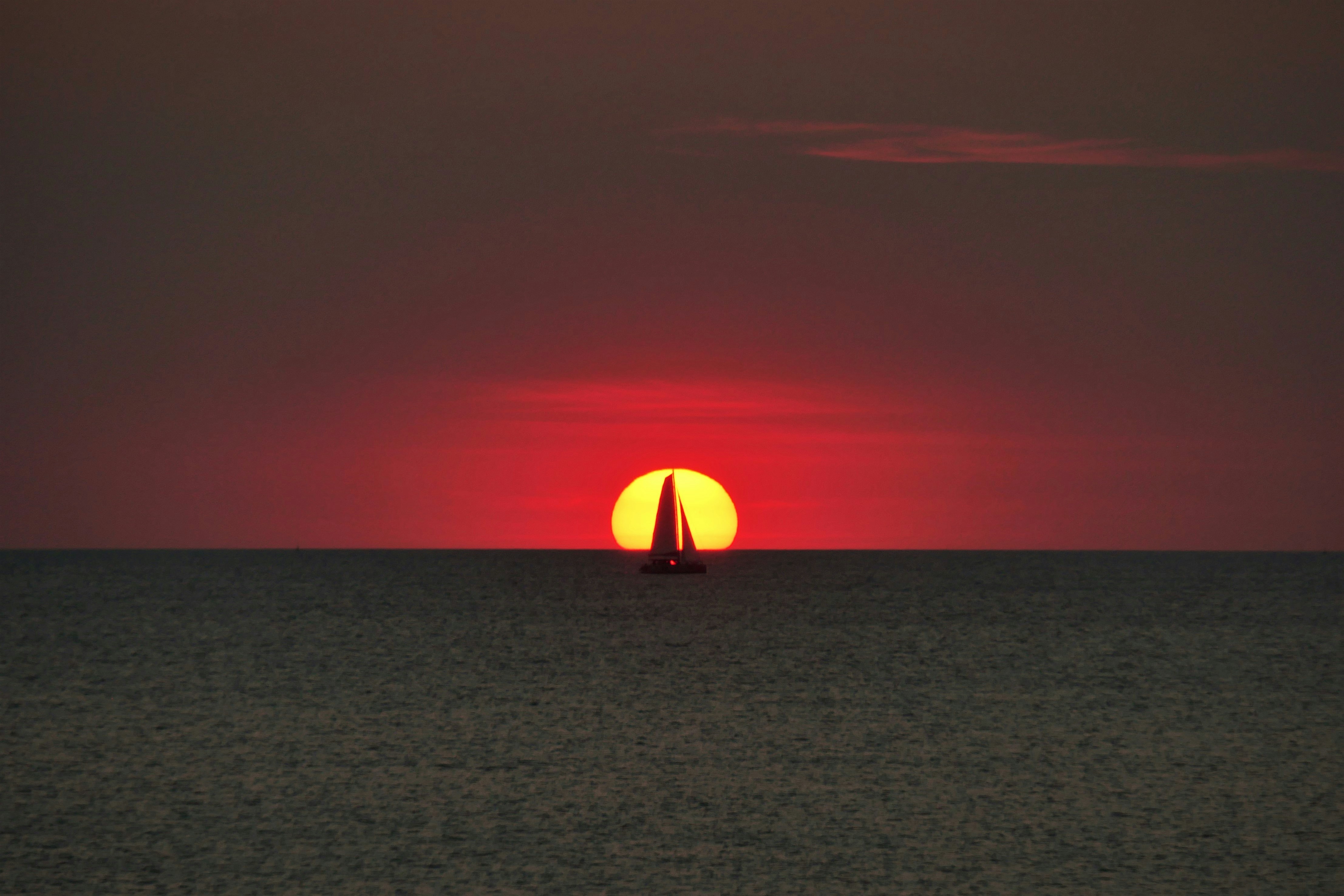 Horizon Ember: A Lone Sailboat at Sunset