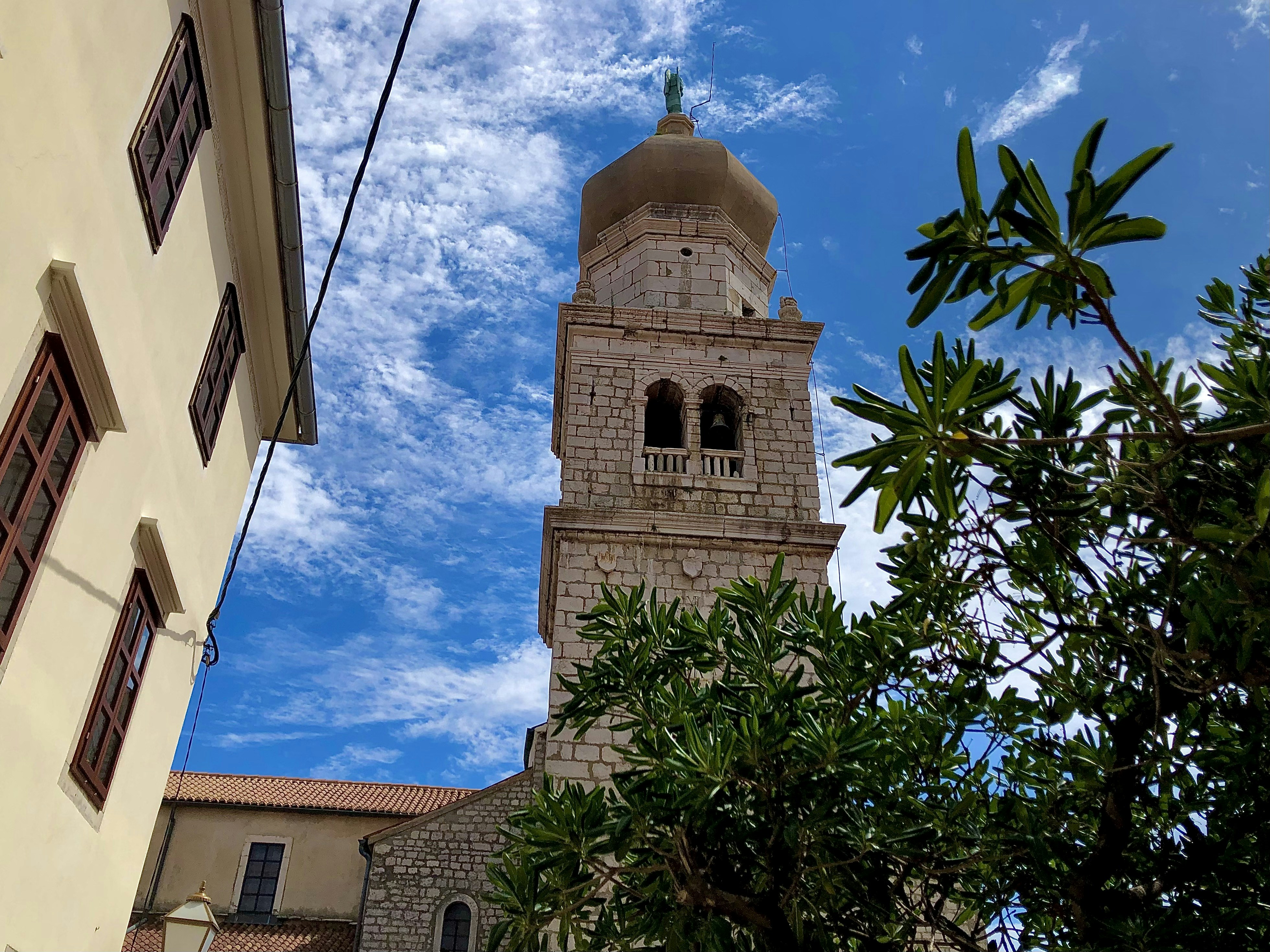 Stone bell tower rises beside lush greenery under a vibrant sky.