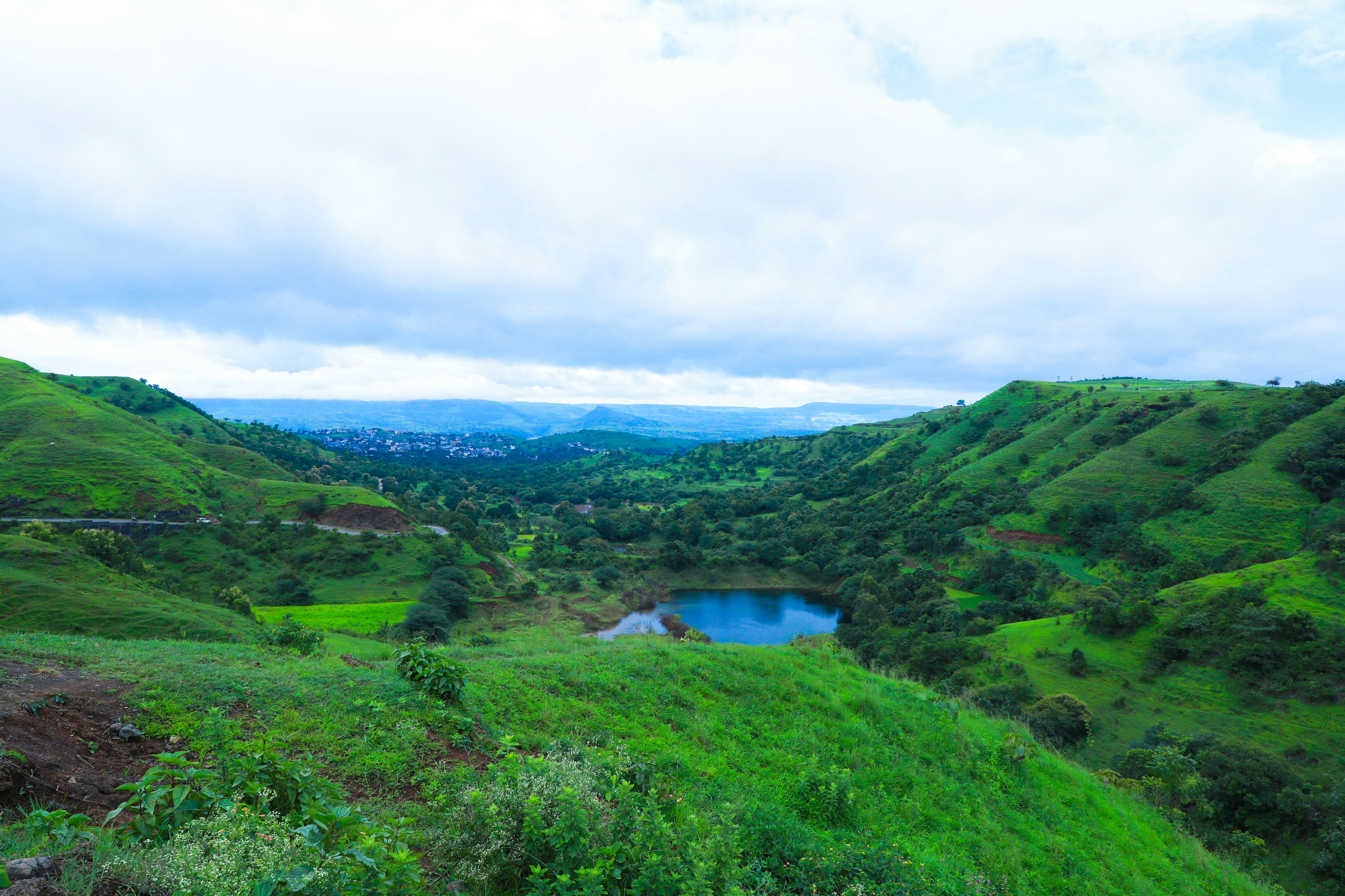 Lush green hills surround a small pond under a cloudy sky.