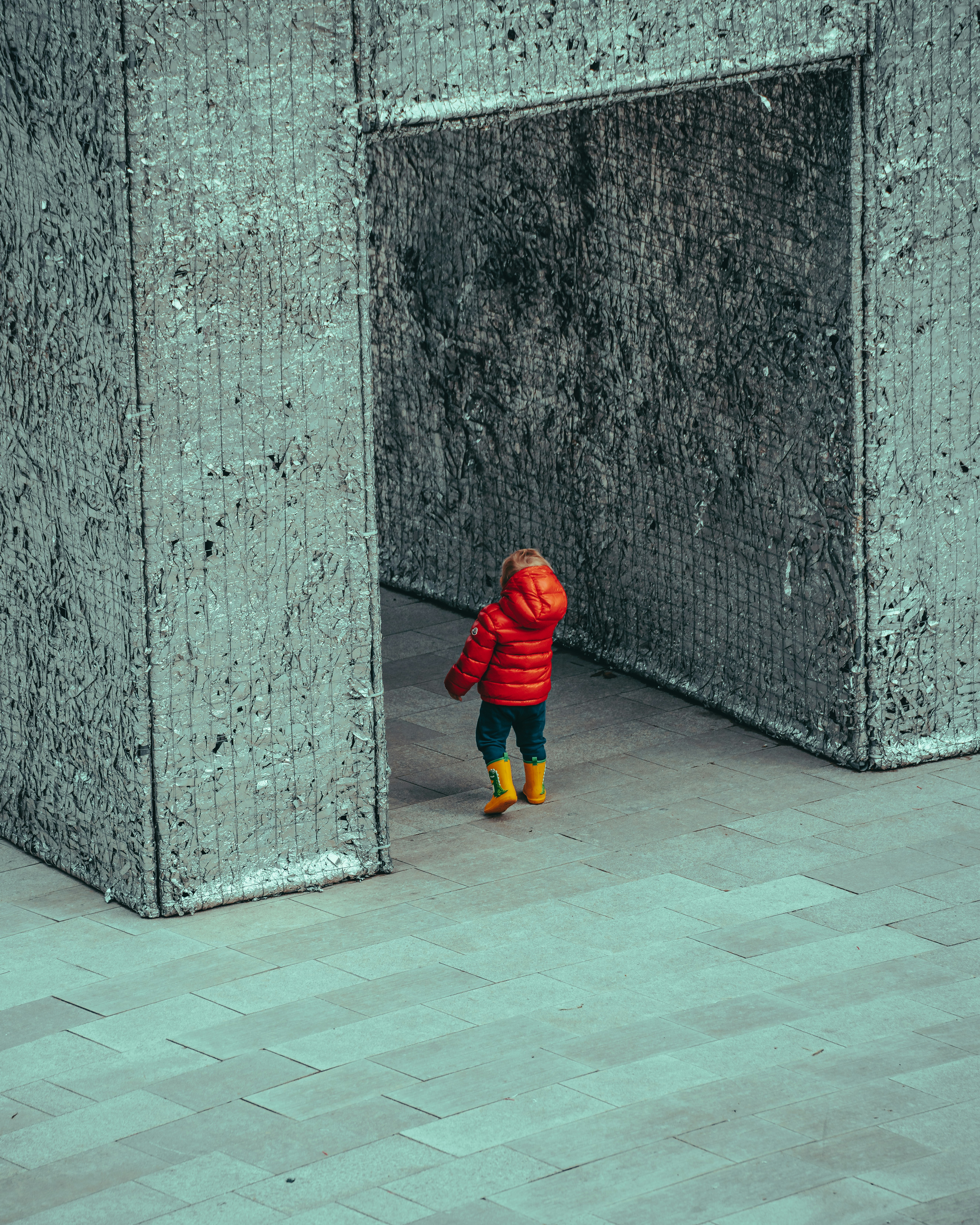Red Coat, Concrete Canopy: A Child’s Quiet Stroll Through Monolithic Gray