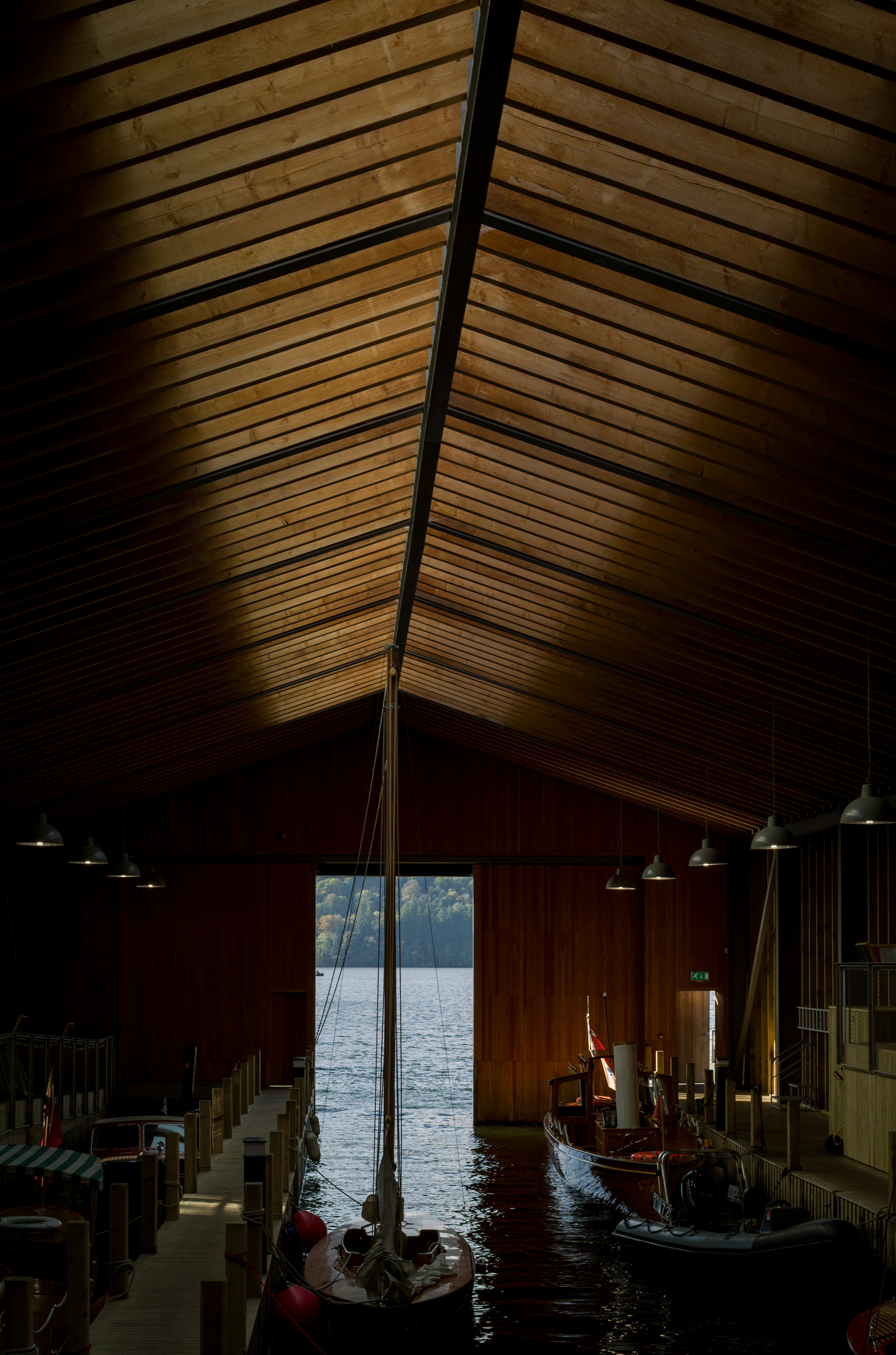A tranquil harbor scene with boats docked inside a wooden structure, illuminated by soft light filtering in from an open doorway leading to a serene waterway.
