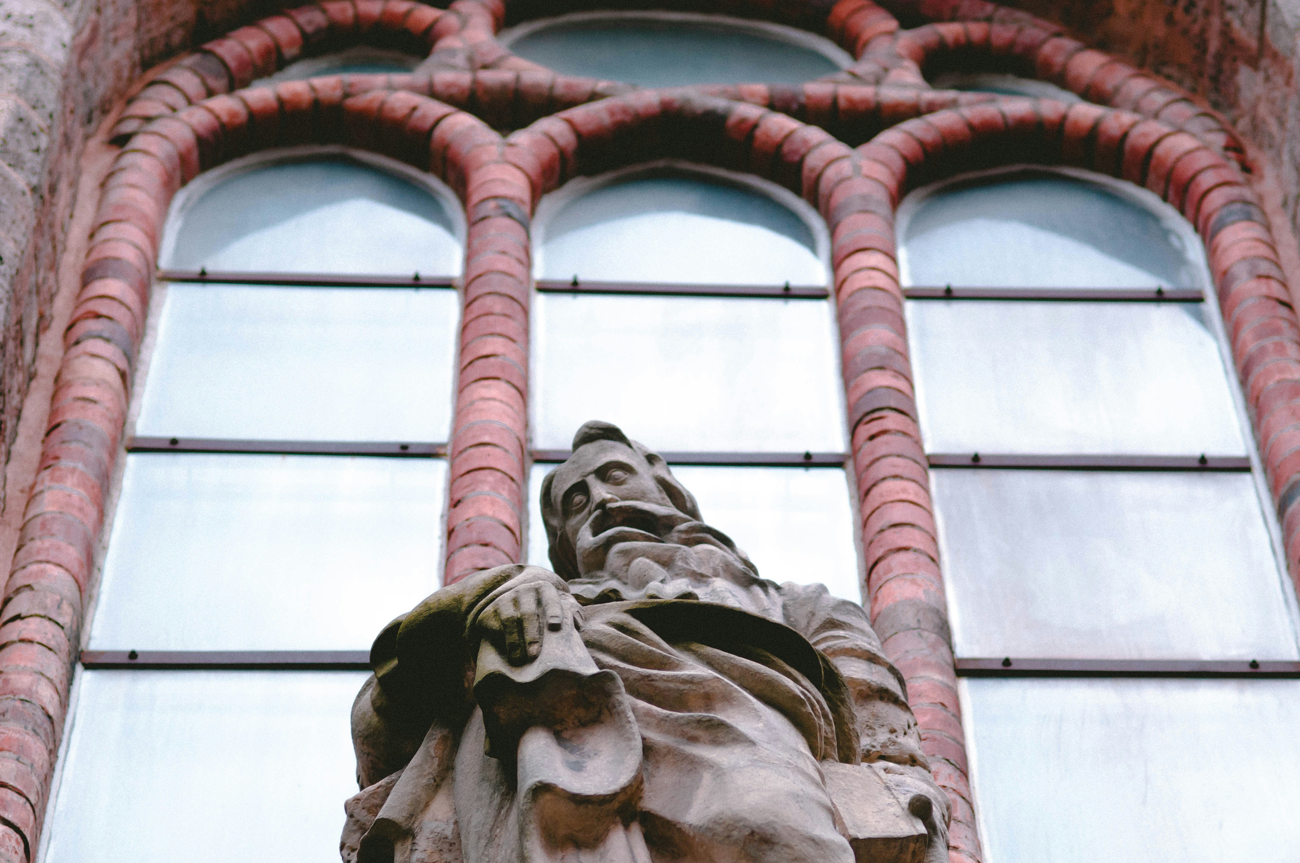 Stone statue of a historical figure against a backdrop of arched windows with red brick detailing.