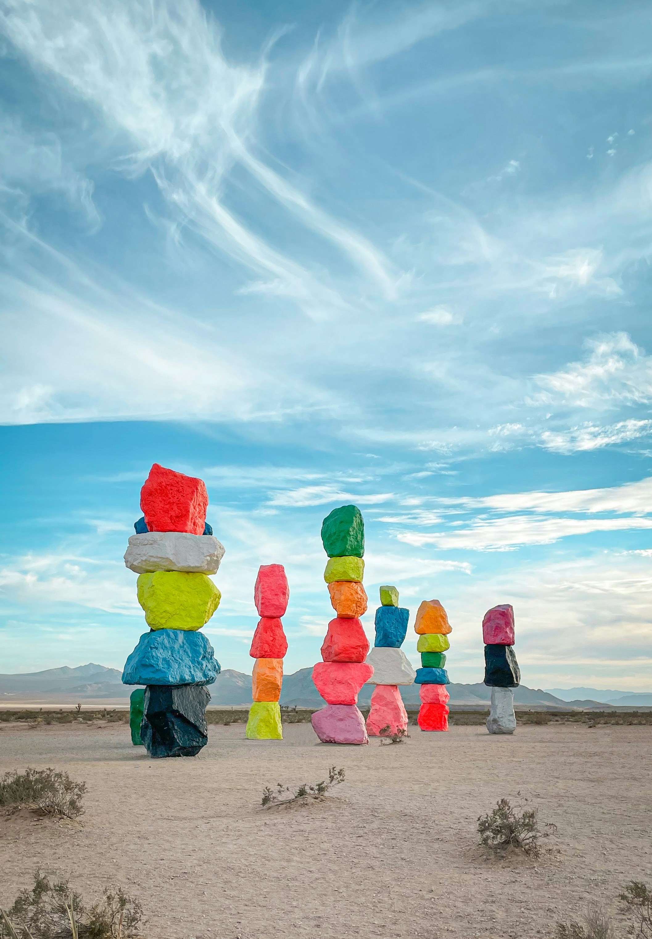 Vibrant stacked rocks in various colors stand prominently in a desert landscape under a dynamic sky.