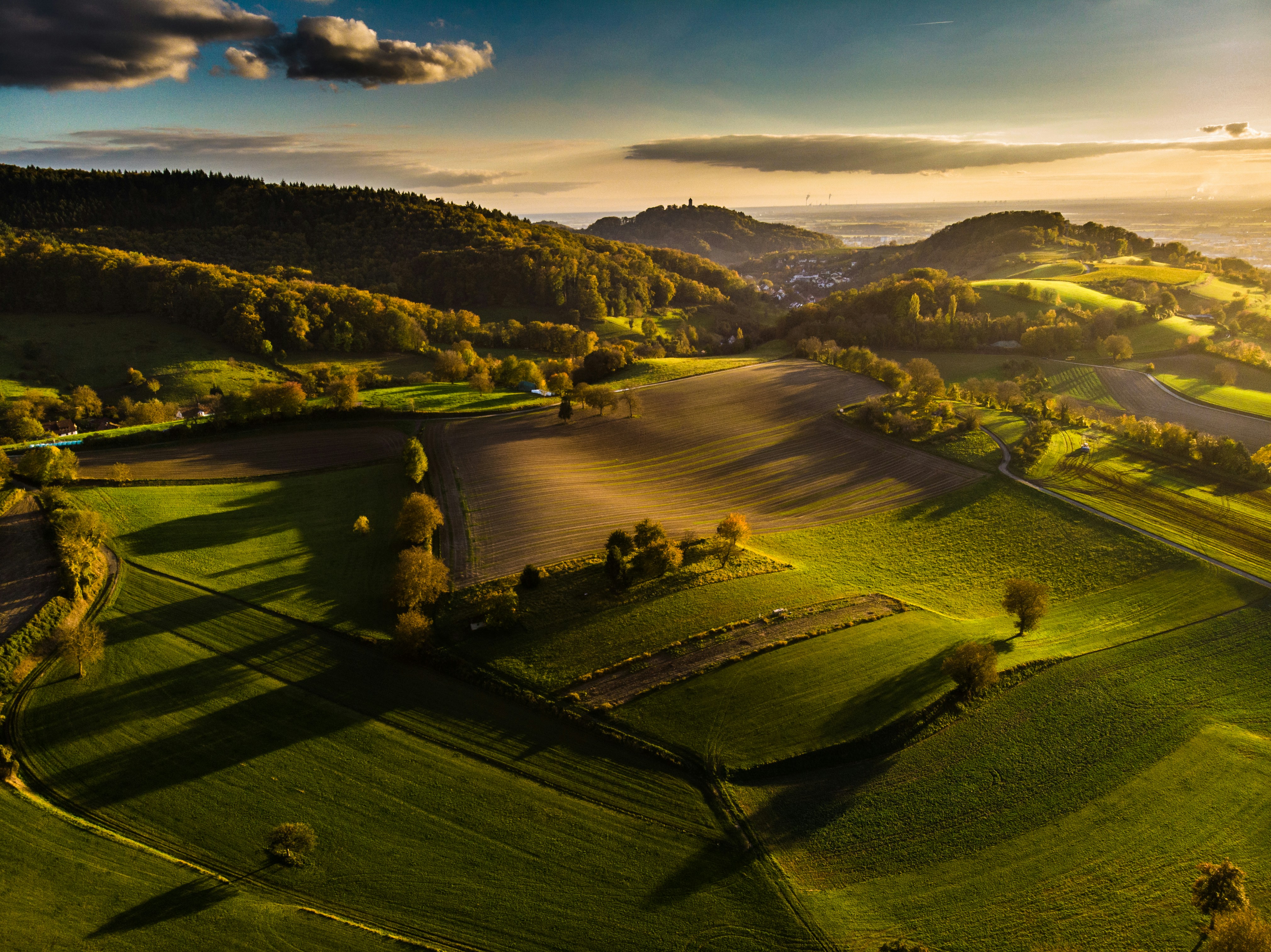 Rural landscape near Bensheim, Germany The photograph, taken at sunset, showcases the rolling hills of the countryside bathed in the warm glow of the golden hour. The long shadows accentuate the textures of the fields, creating a tapestry of natural beauty. | an aerial view of rolling hills and rolling fields