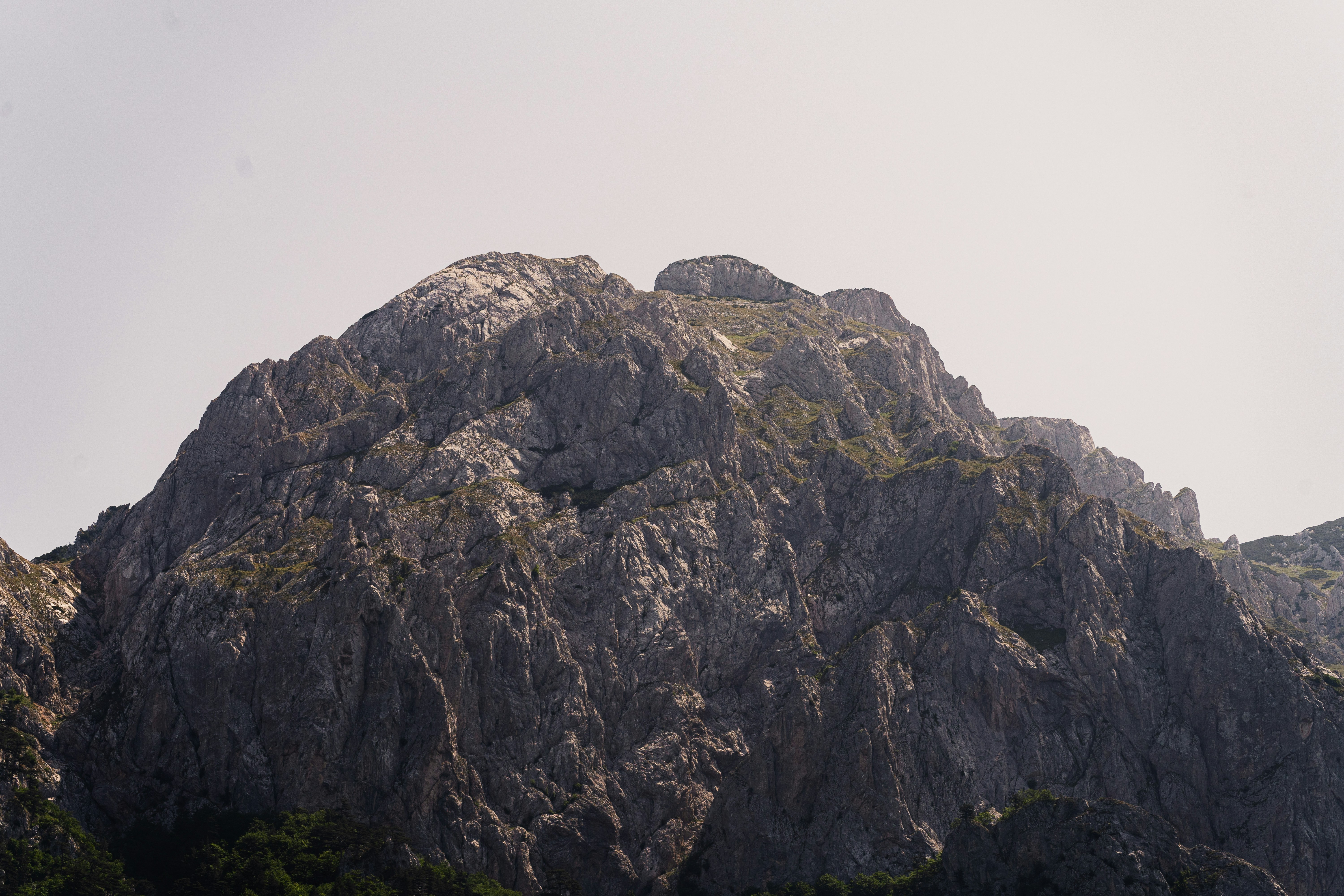 Imposing mountain peak showcasing rugged rock formations and lush greenery at its base.
