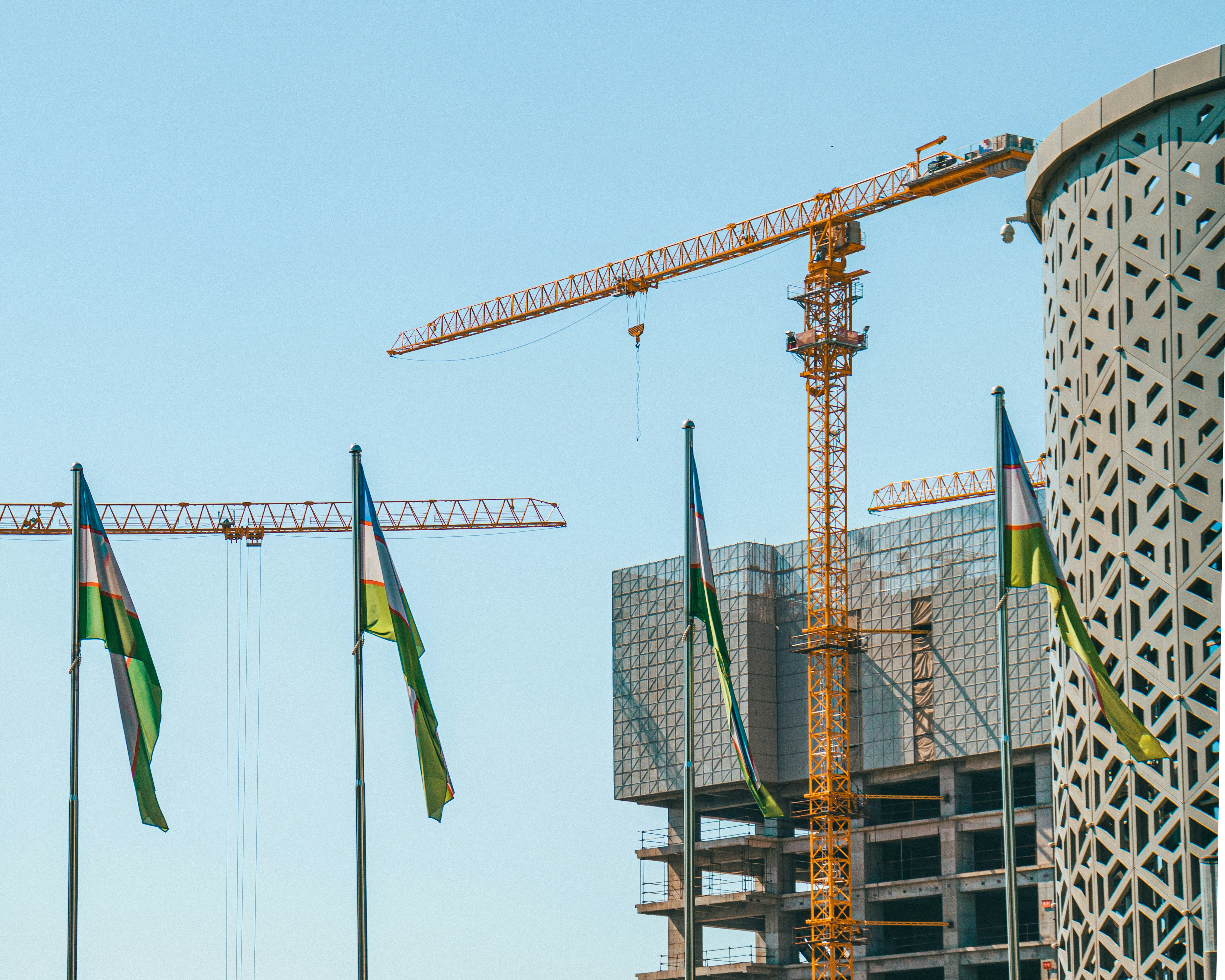 Construction crane towering over a modern building facade with national flags in the foreground.