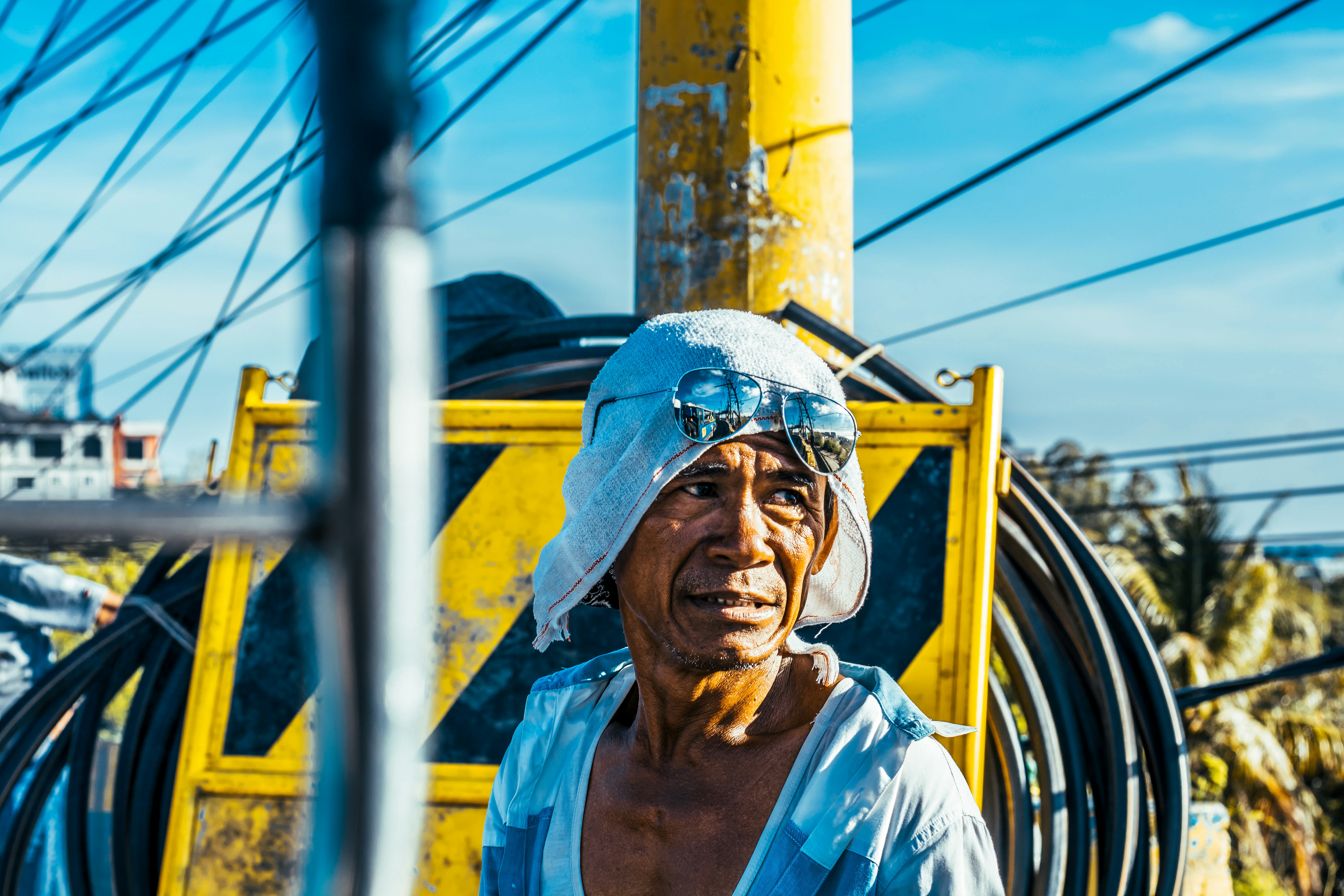 Eyes on the Coil: A weathered worker framed by yellow rigging and blue sky