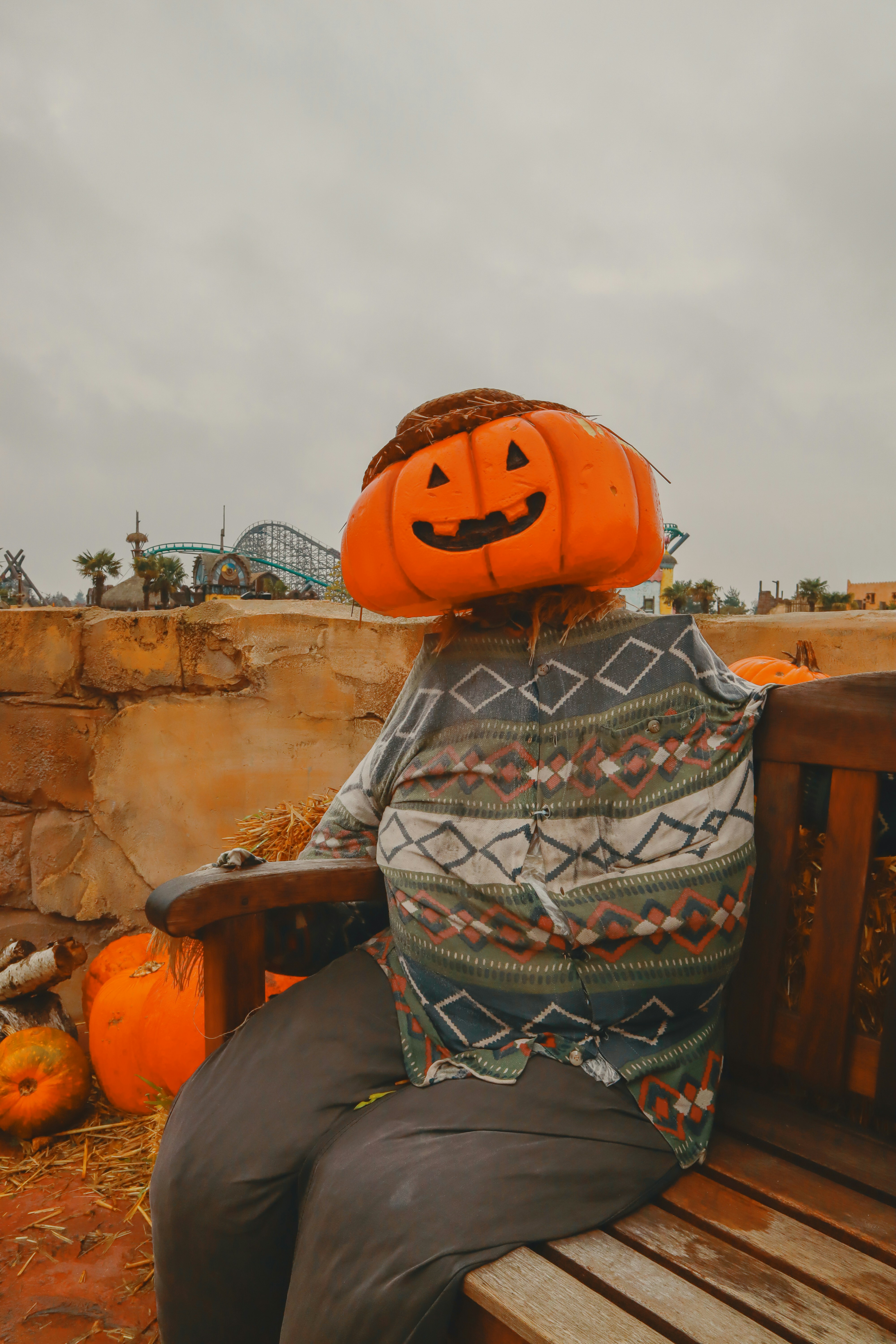 Pumpkin-Headed Figure on a Weathered Bench Under an Autumn Sky