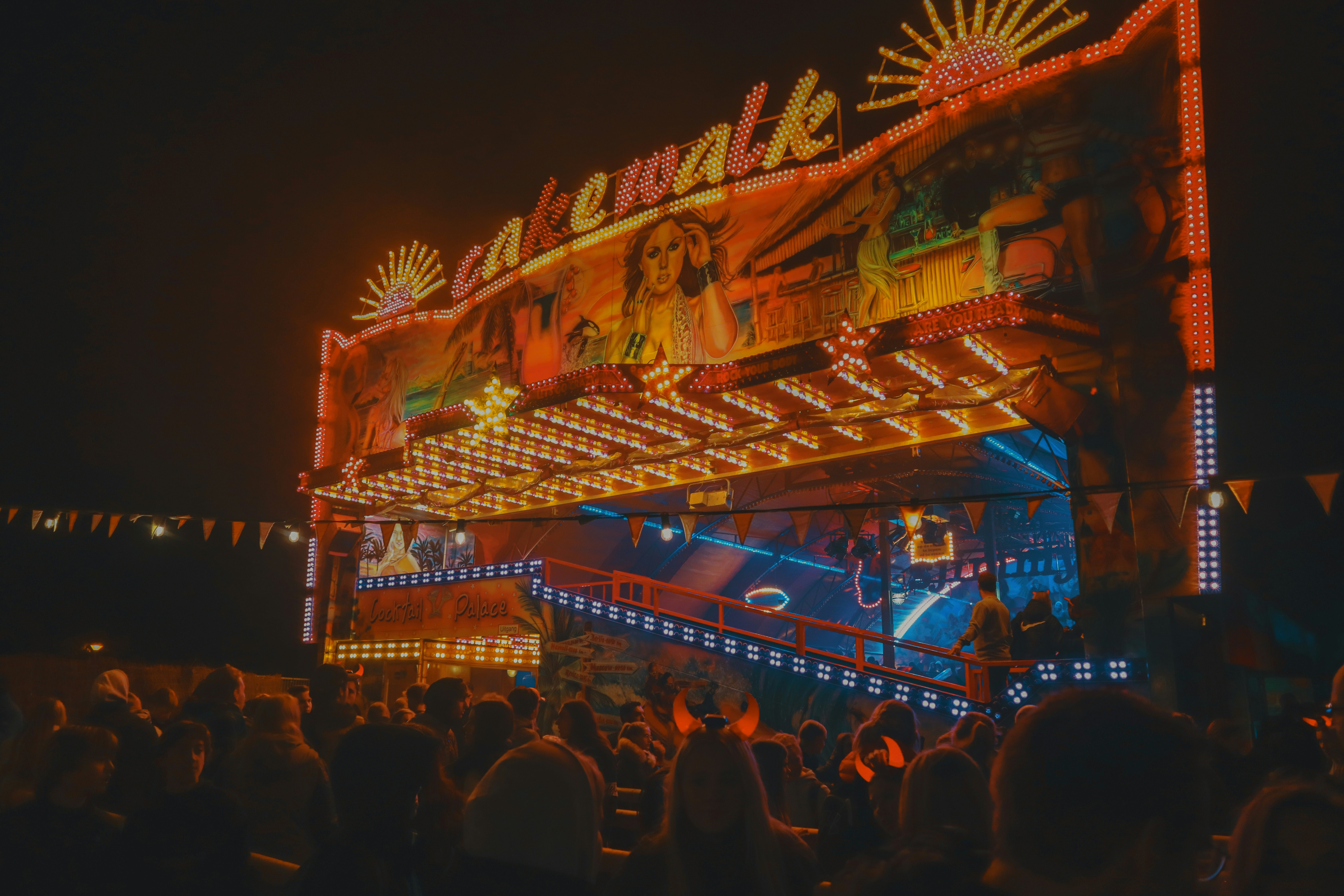 Crowd gathers under vibrant neon lights of a colorful carnival ride at night.
