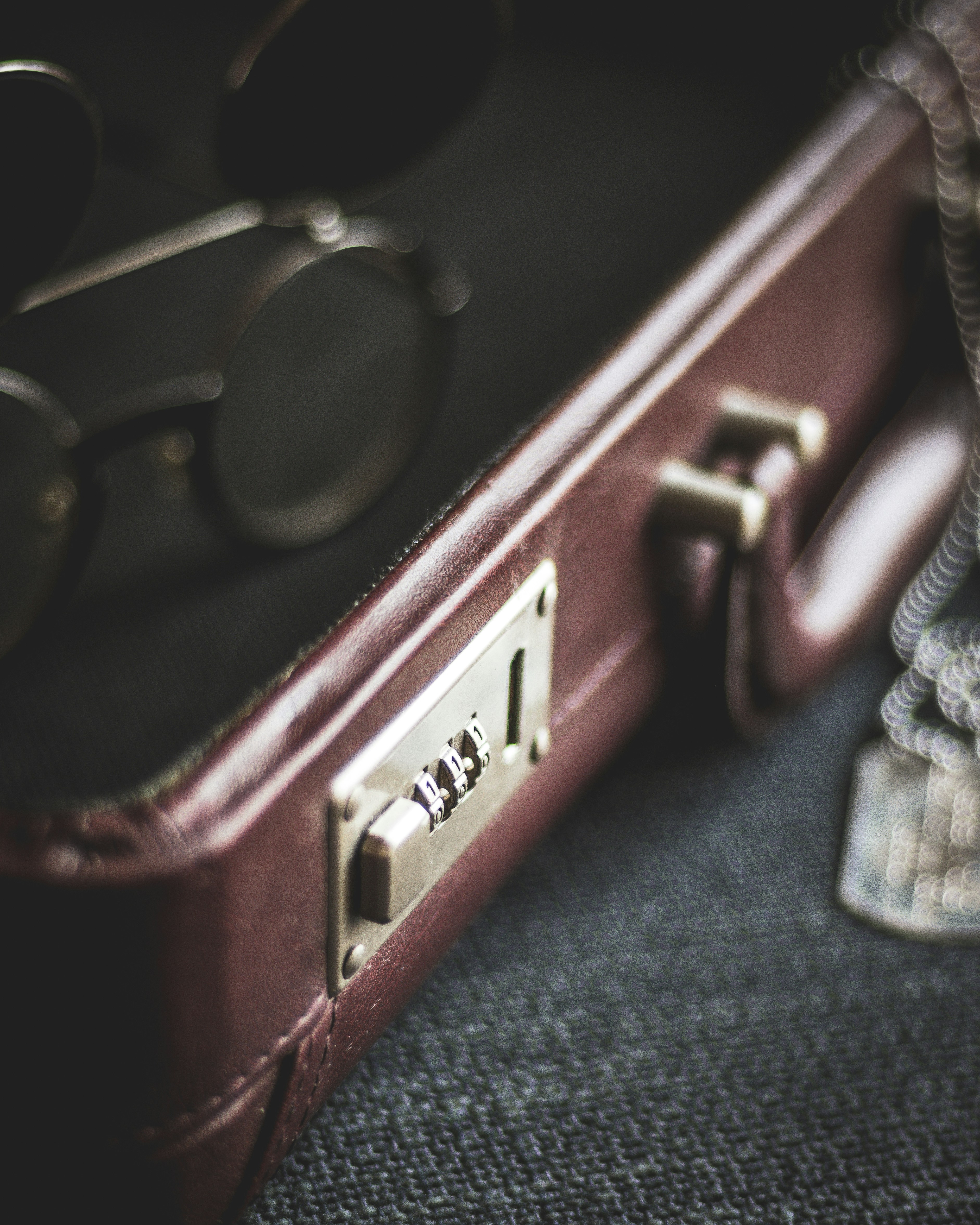 Close-up of a vintage suitcase with a combination lock, accompanied by round sunglasses resting nearby.
