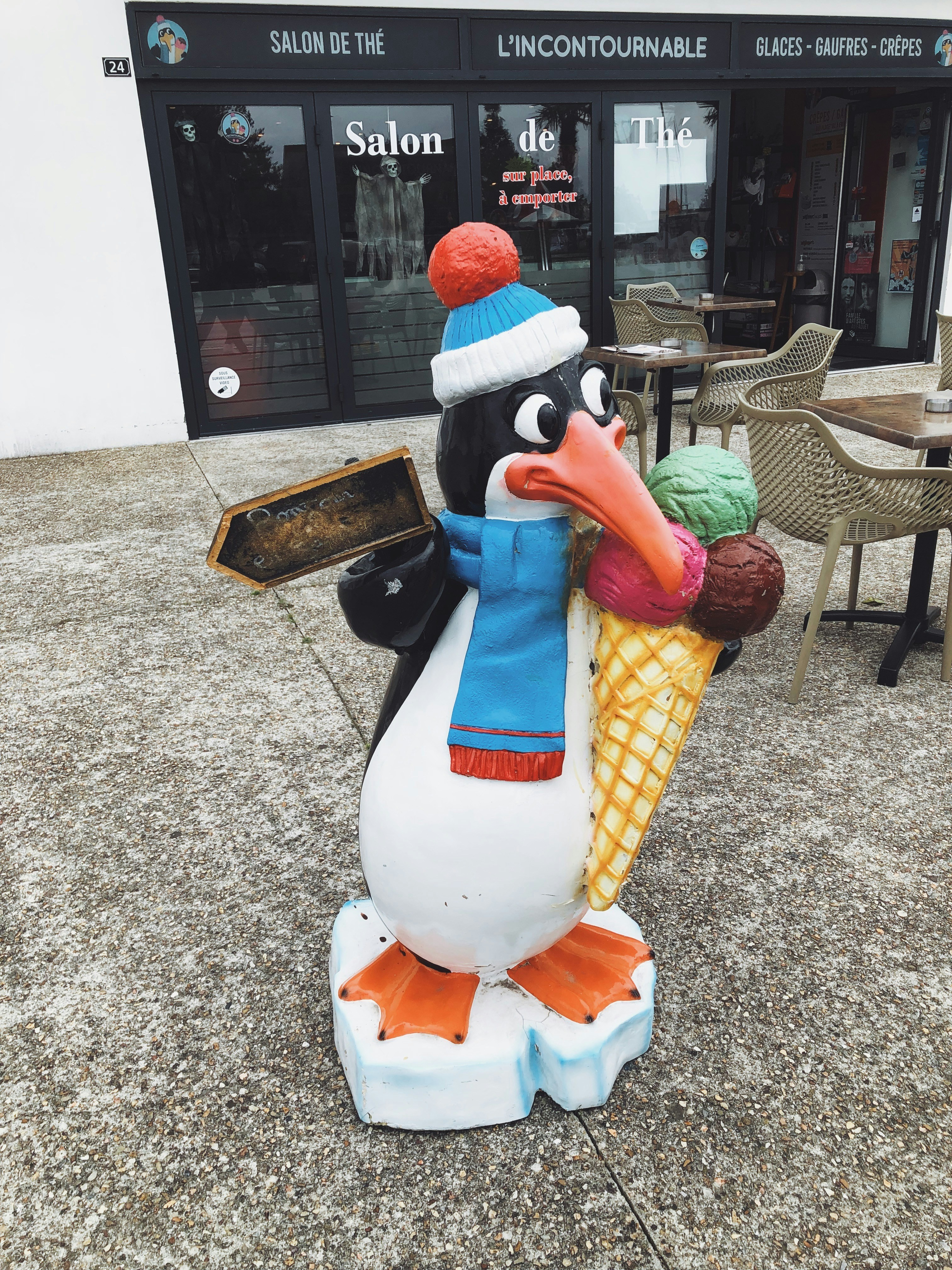 Scoops and Snow at Café de Thé: Penguin Statue in Colorful Winter Attire