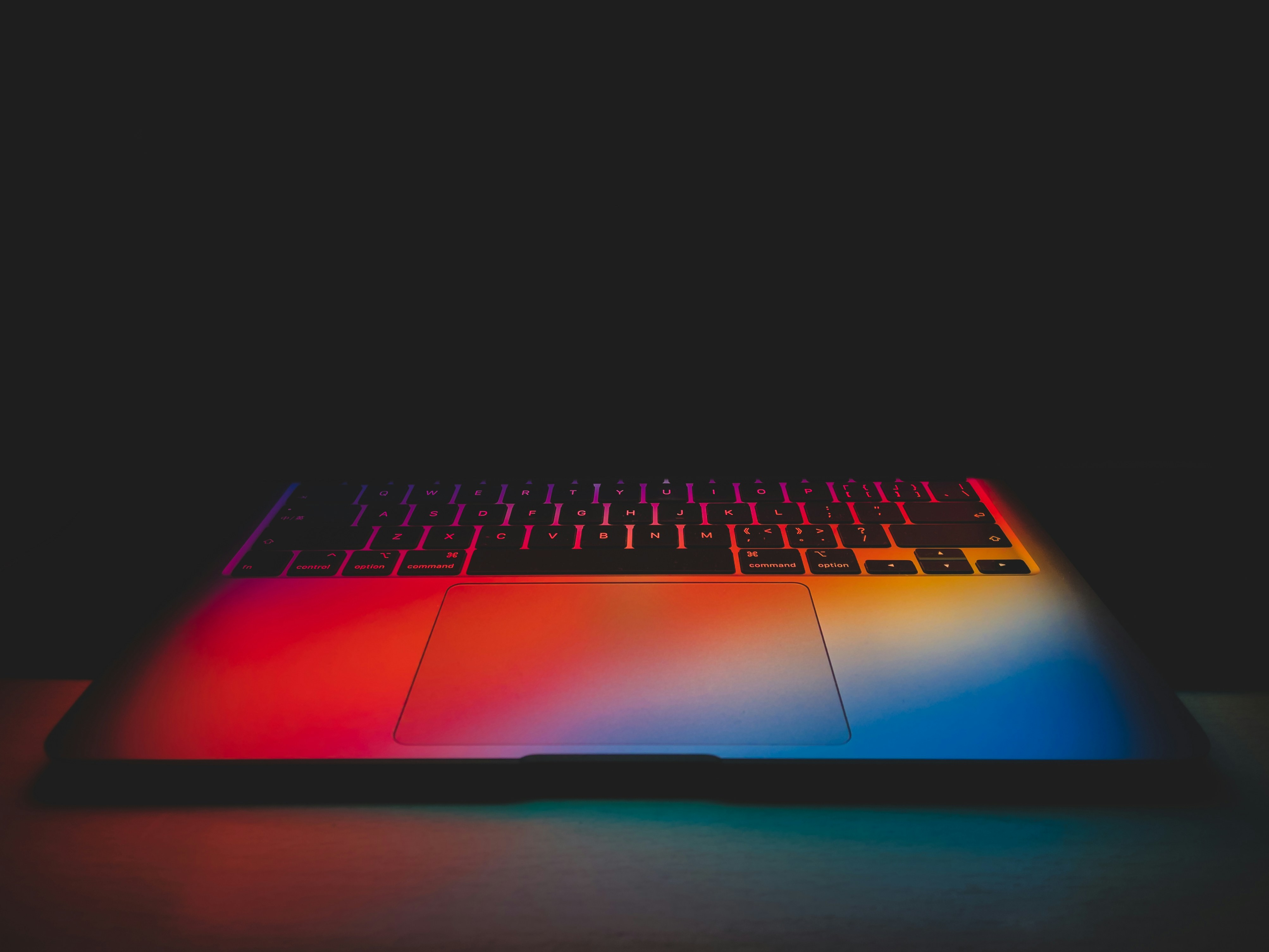 A sleek laptop illuminated by vibrant, multi-colored light against a dark backdrop, showcasing its elegant design and modern aesthetics.