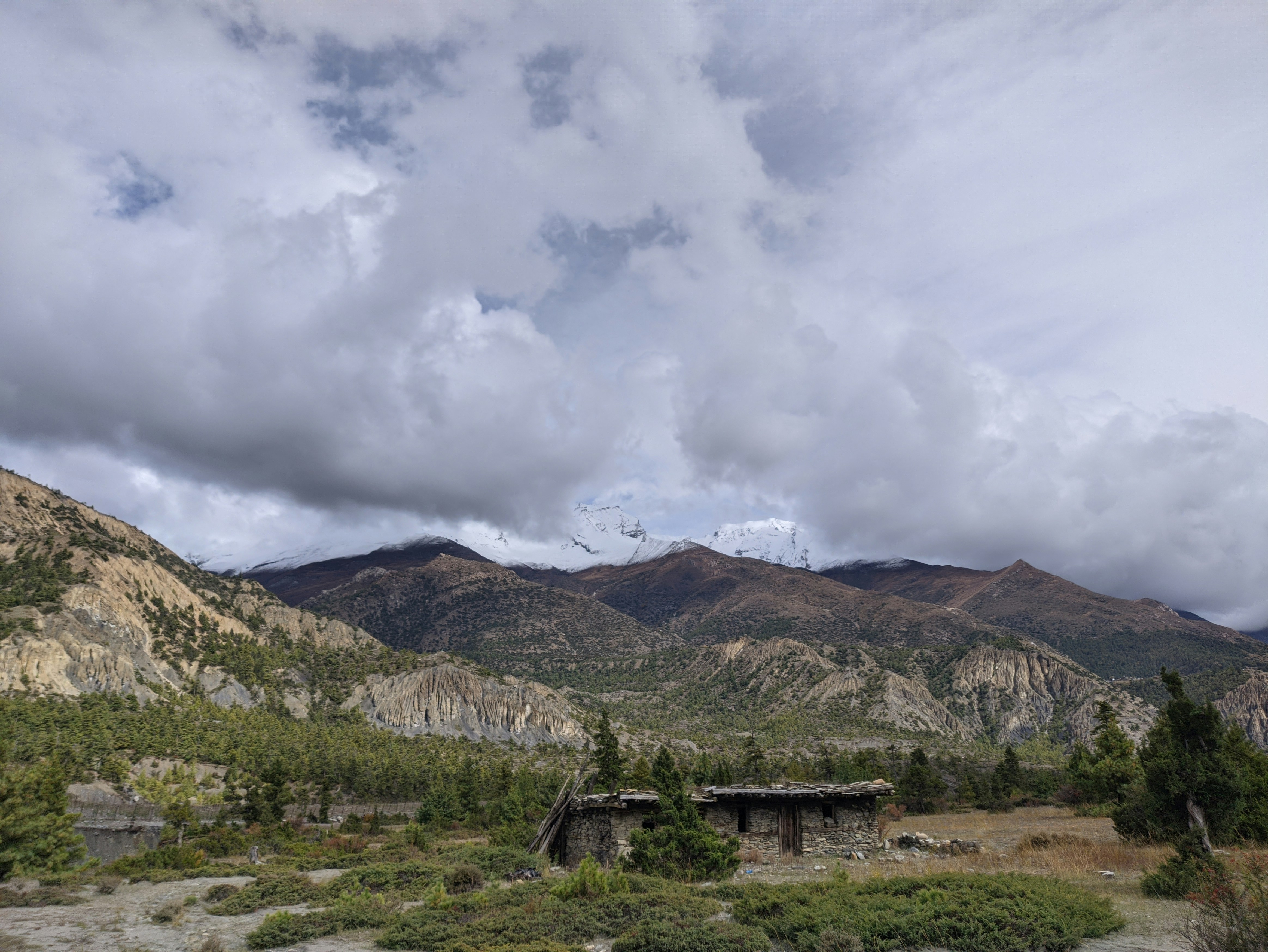 High plain with a stone hut, rolling hills and big clouds on the Annapurna Circuit.