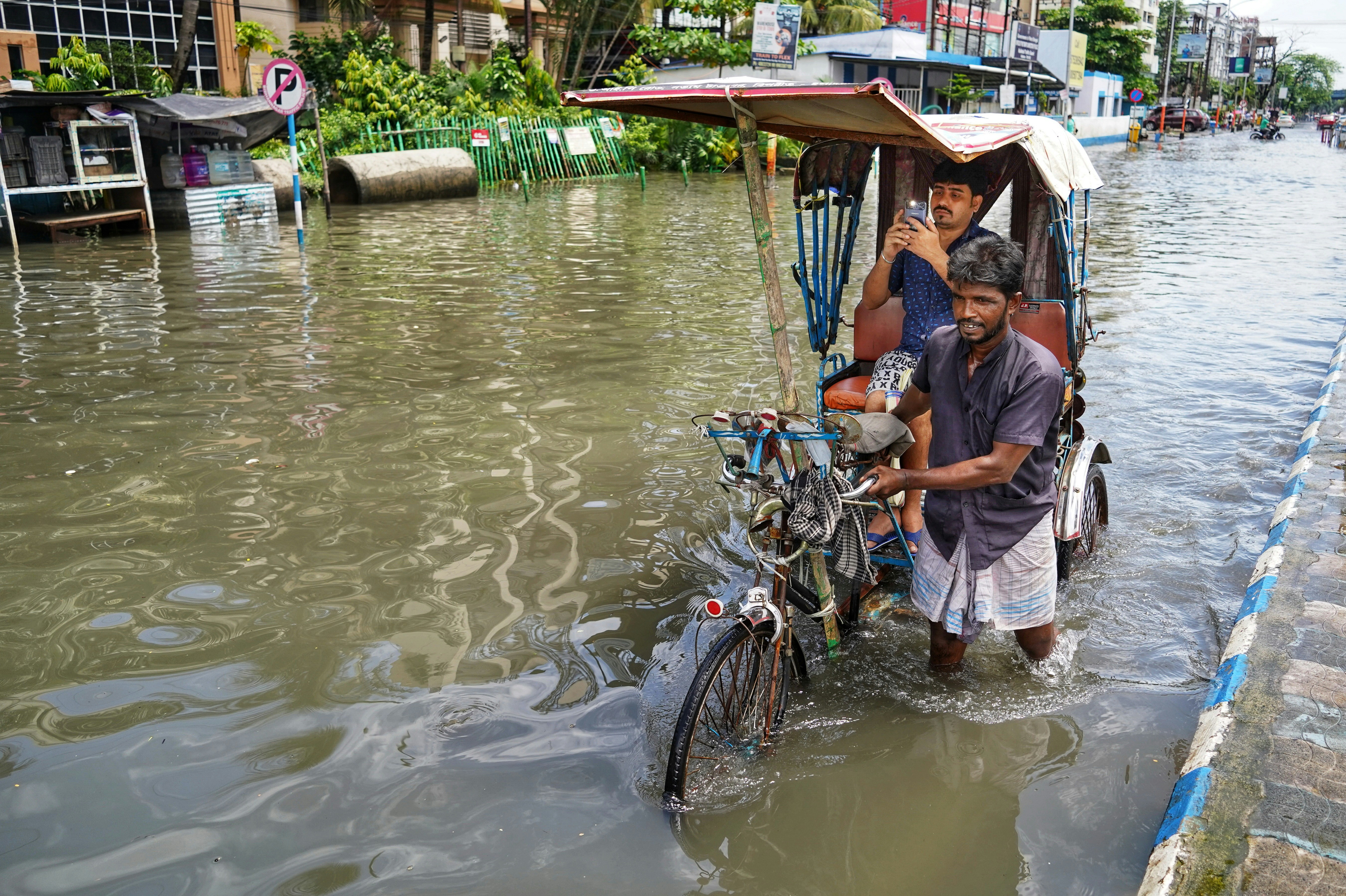 Man pushing a bicycle rickshaw through a flooded city street.