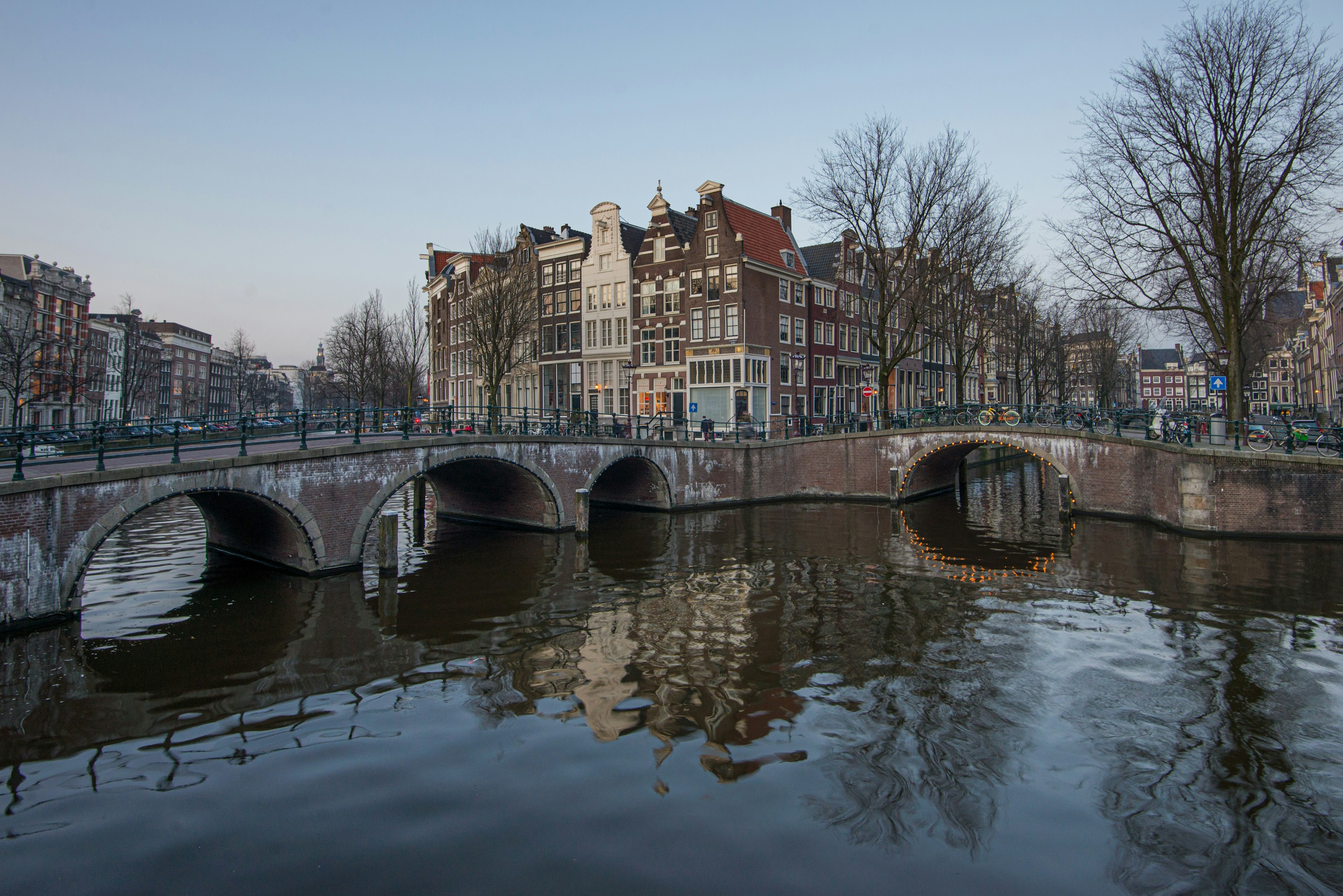 Historic canal houses and arched bridge reflected in Amsterdam's Keizersgracht canal during twilight.