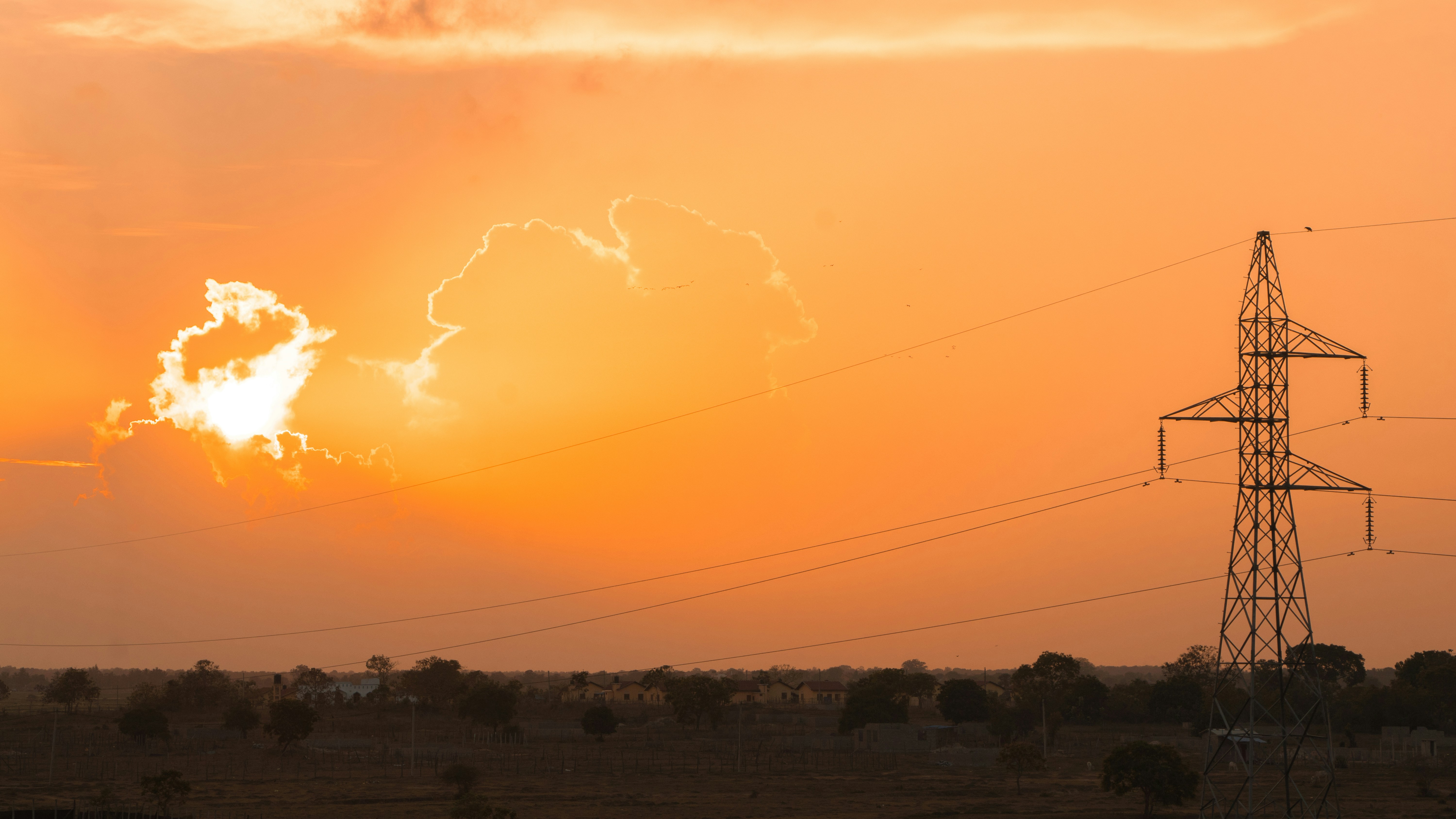 Electric tower stands against a vivid orange sunset with scattered clouds.